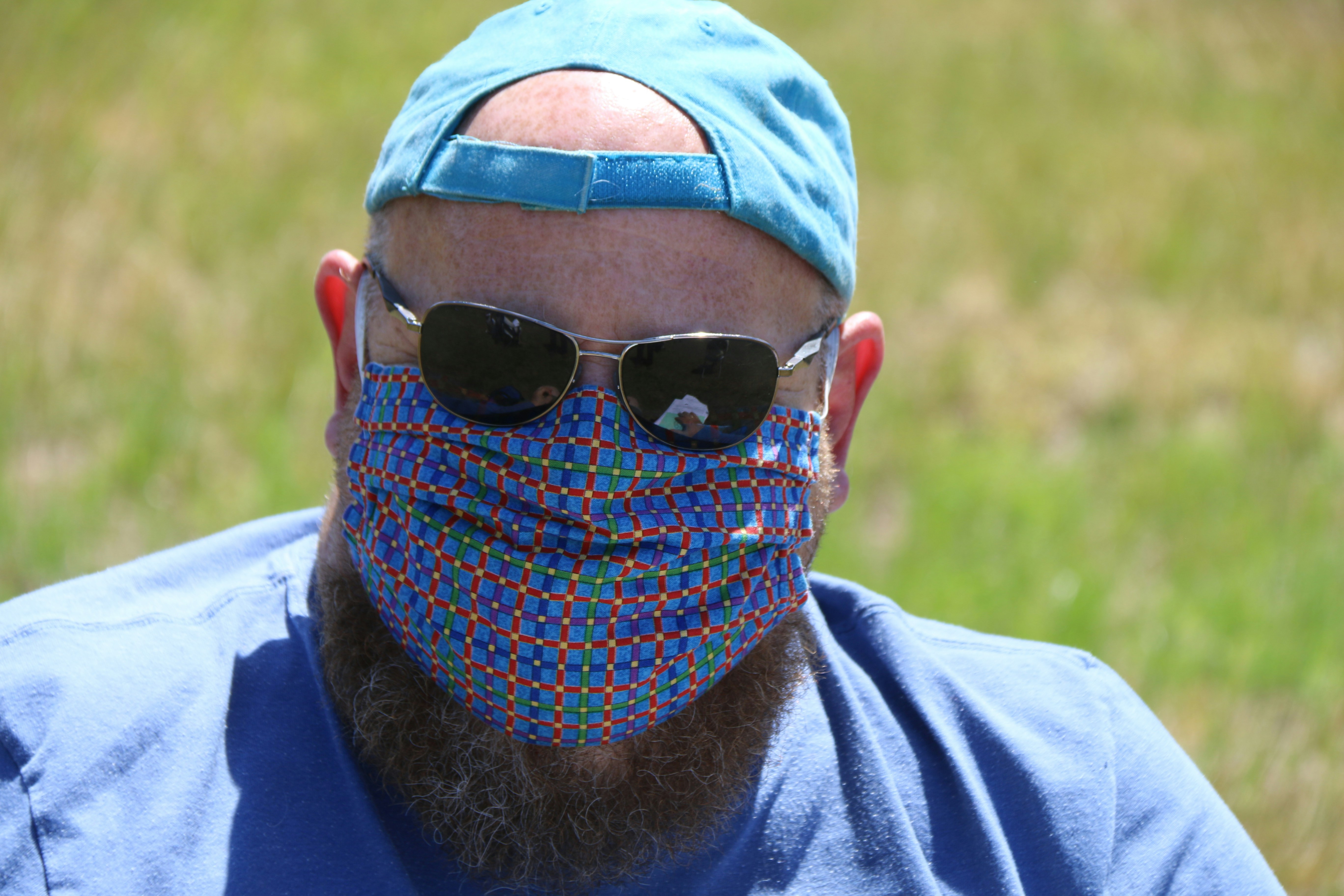 Blue Cap Portrait: Bearded Man in Sunglasses and Patterned Mask in a Sunlit Field