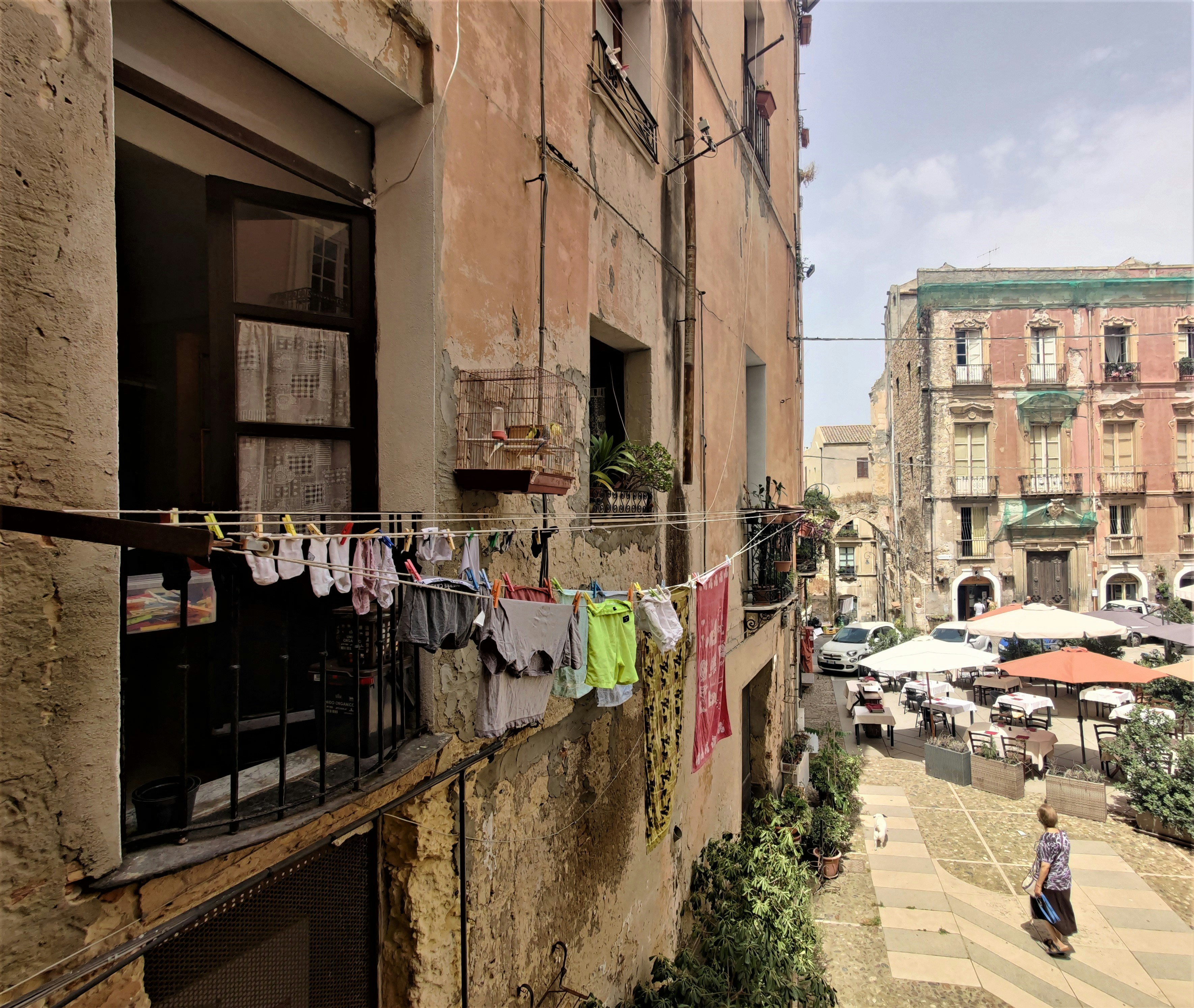 Clothes hanging on a line outside an aged apartment building overlooking a lively street with market stalls.