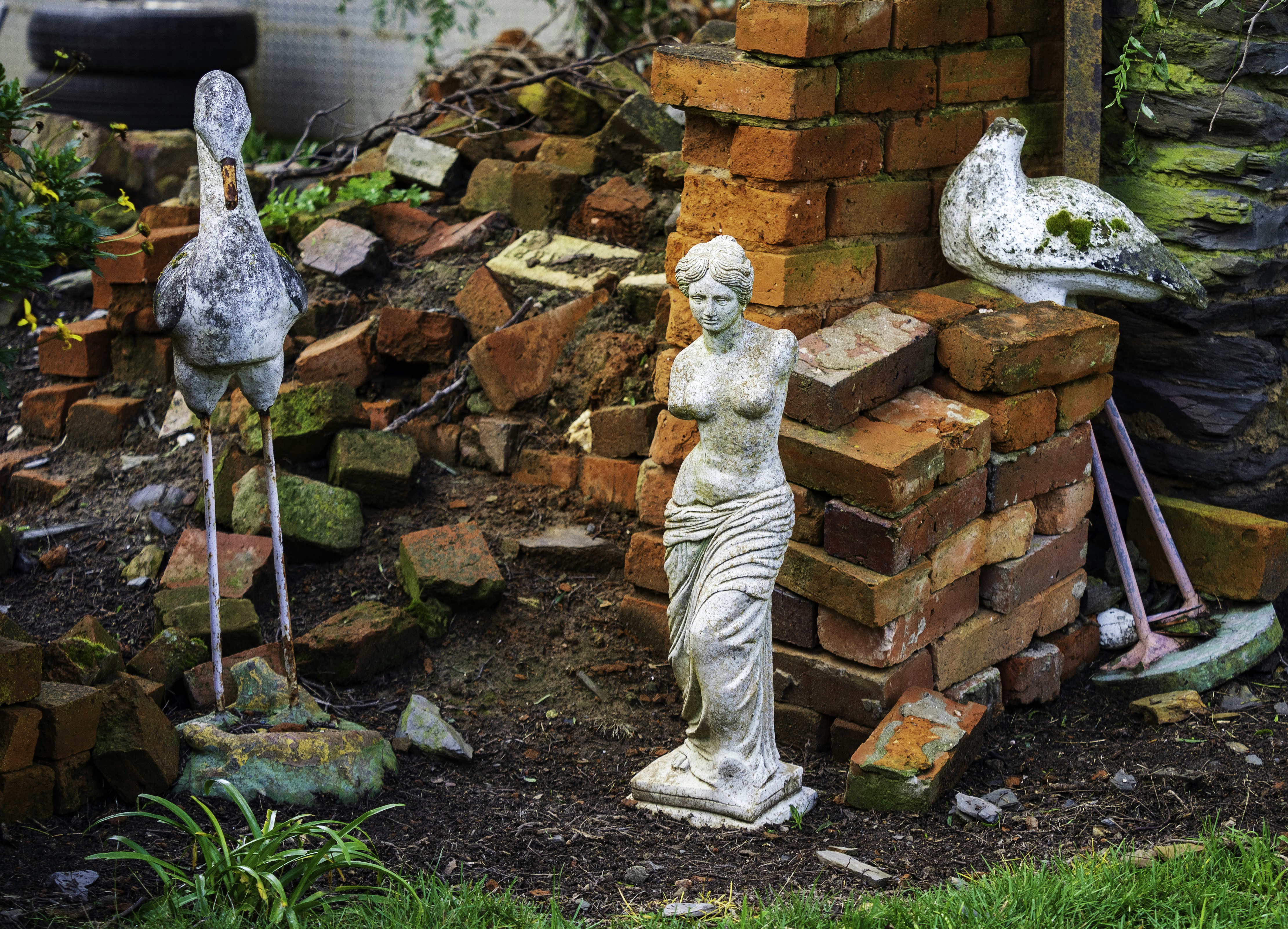 Stone Muse Among Bricks: A Garden Scene Framed by Weathered Bird Sculptures