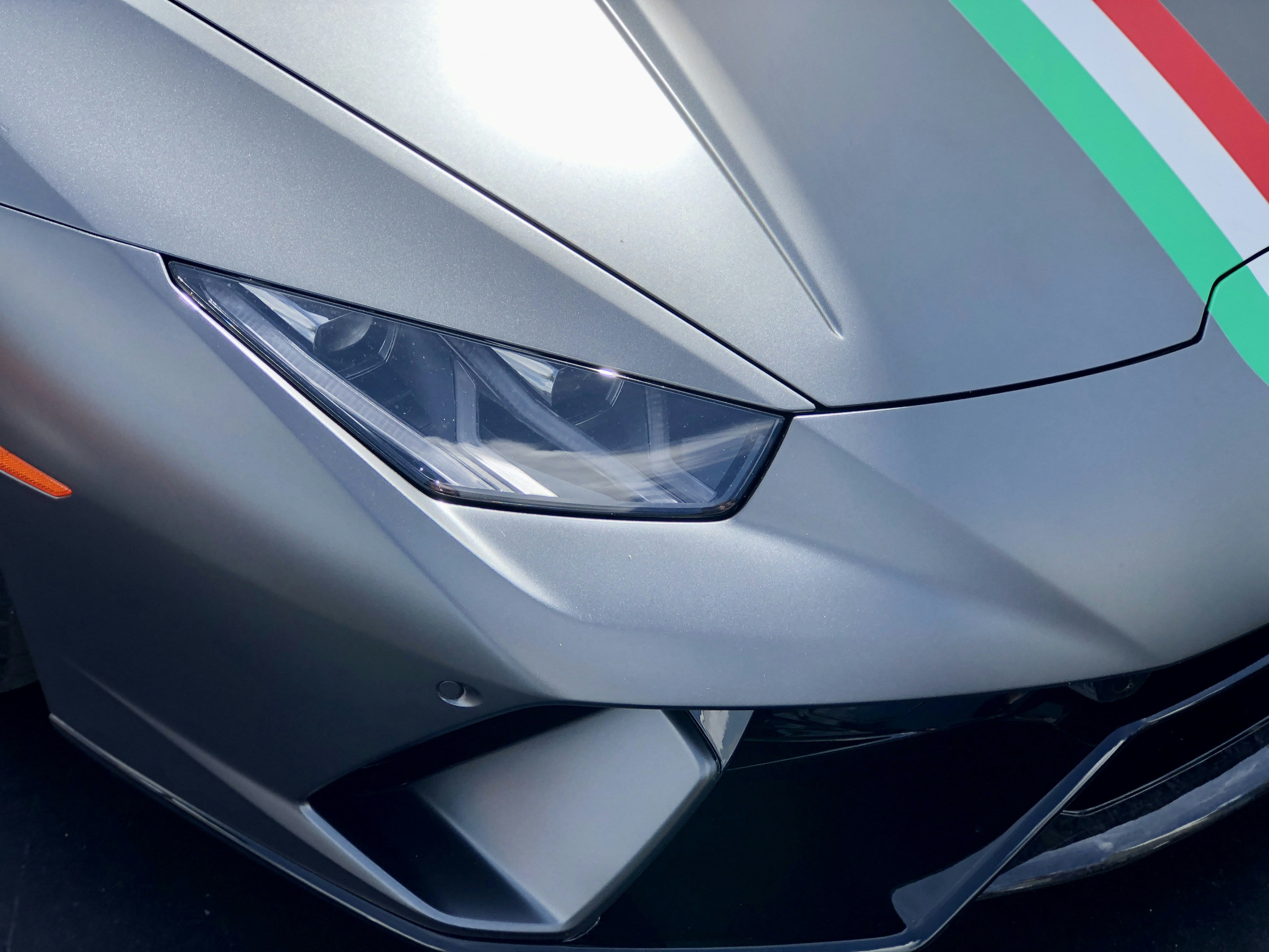 Close-up of a Lamborghini Huracán's angular headlight and front design adorned with an Italian flag stripe.