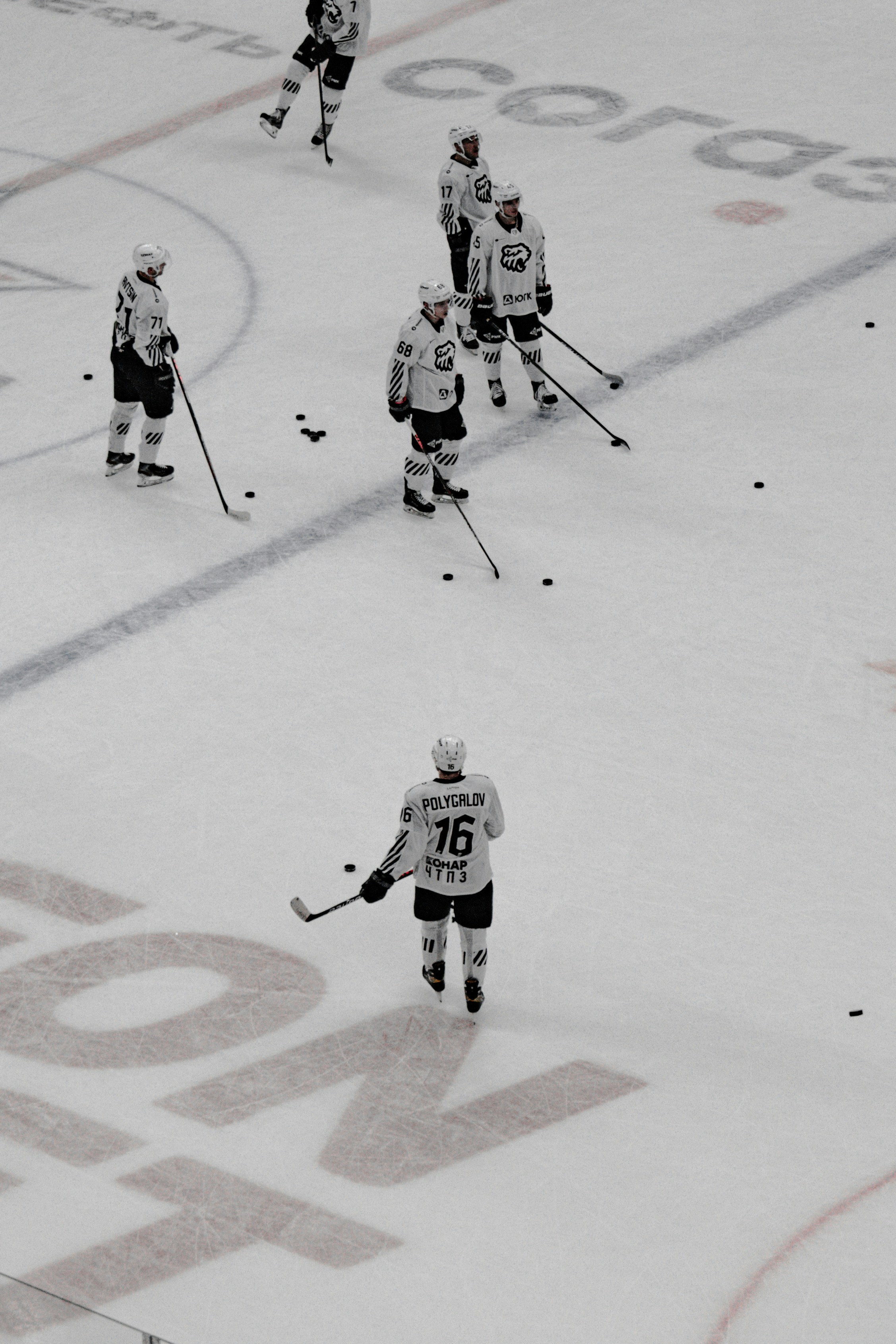 Hockey players practicing on the ice, surrounded by scattered pucks, showcasing their focus and teamwork before a match.
