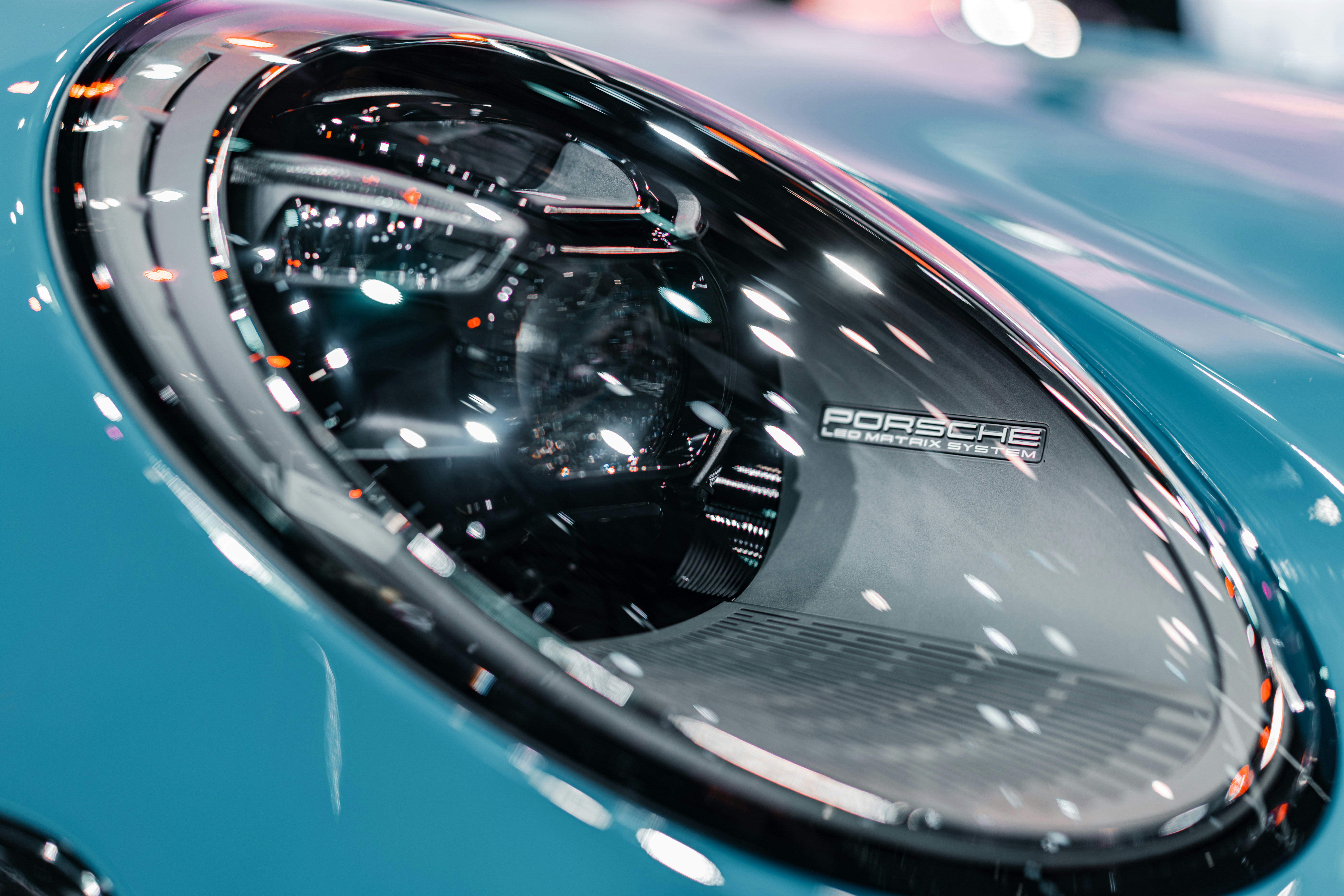 Close-up of a Porsche headlight showcasing intricate design and branding. The sleek lines and reflections highlight the craftsmanship of modern automotive engineering.