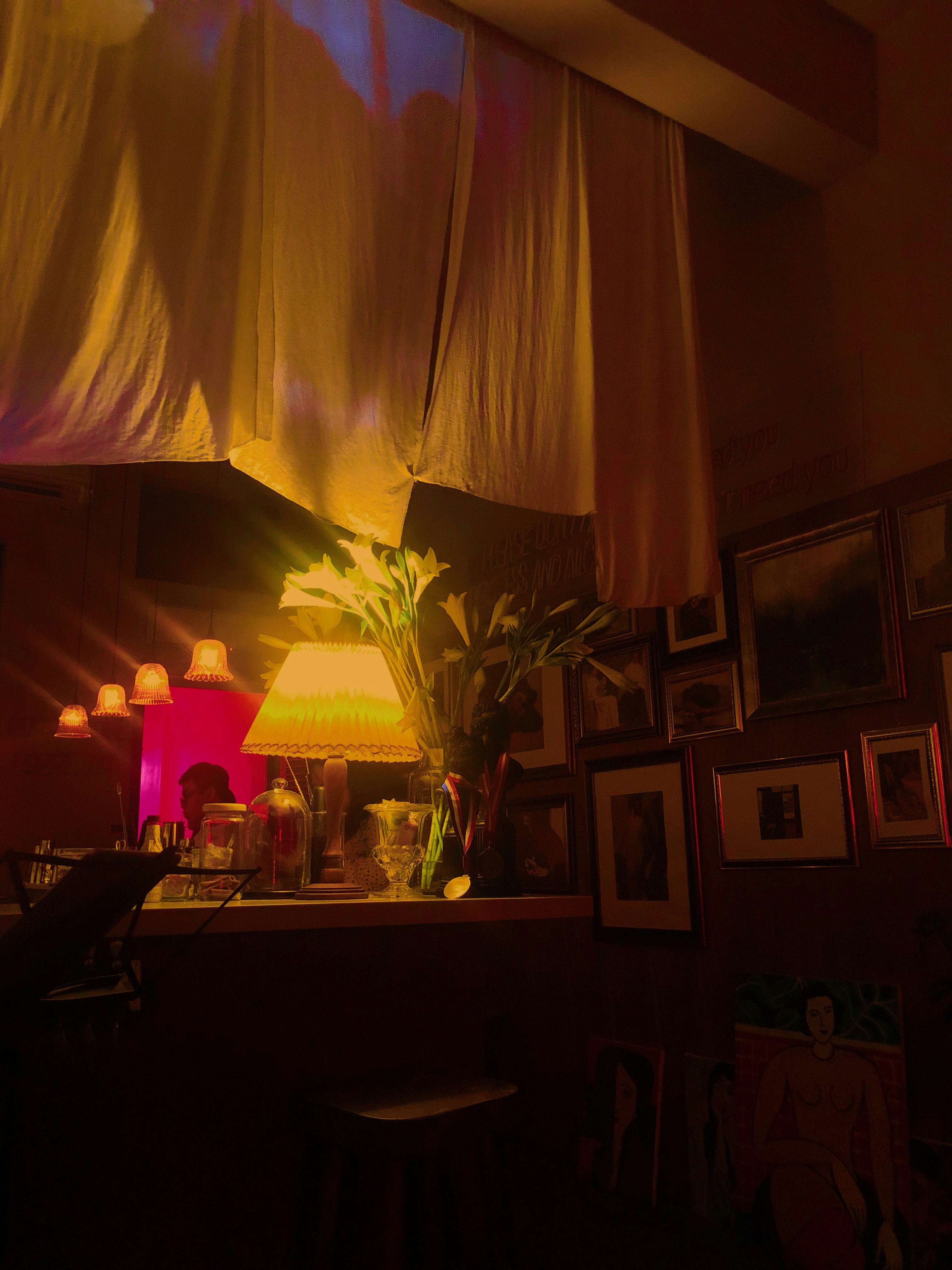 A cozy interior scene illuminated by soft lamp light, featuring a bouquet of lilies and draped fabric, creating a warm, inviting atmosphere.