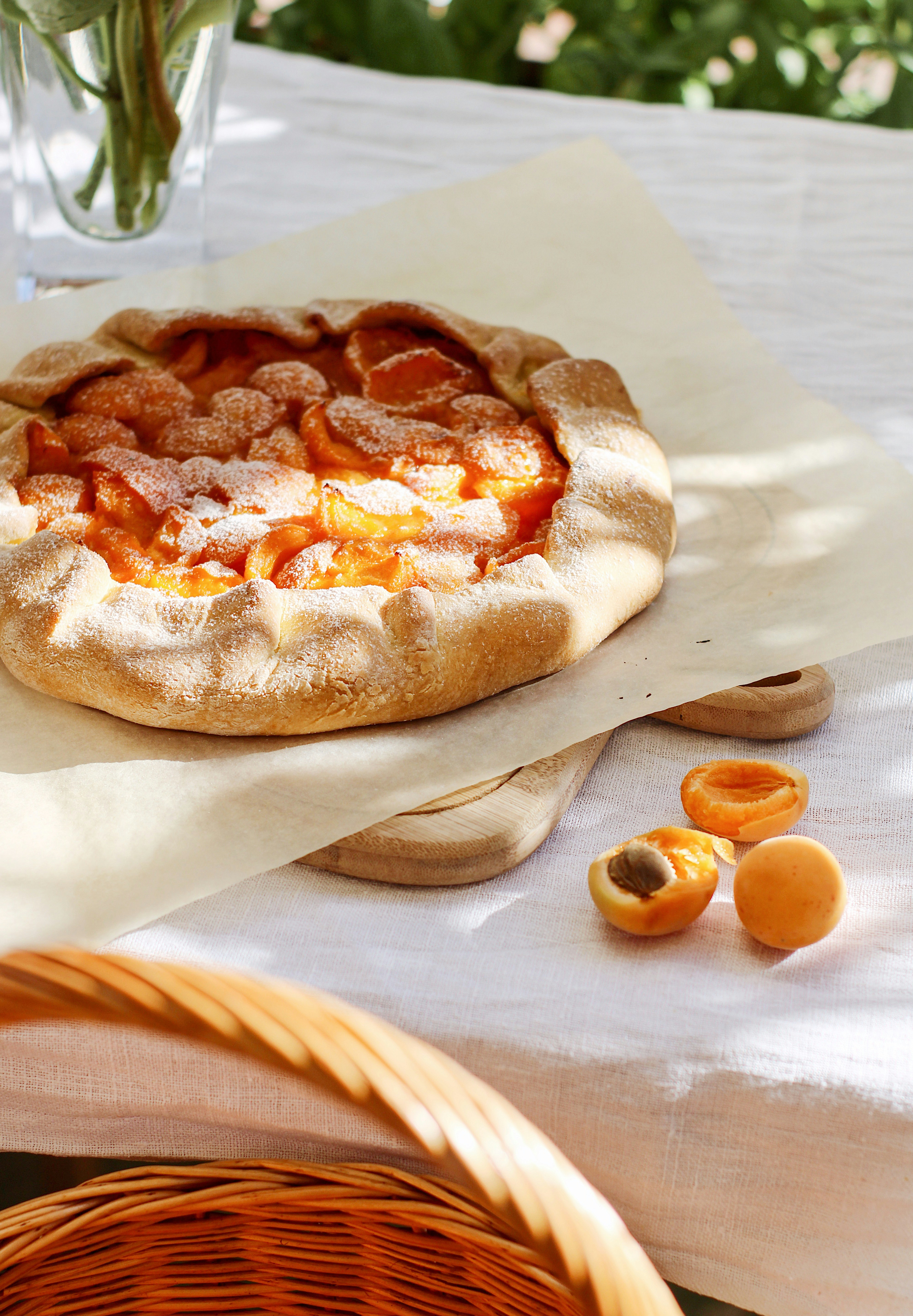 Freshly baked apricot galette resting on a wooden board, surrounded by apricot halves and a basket, showcasing a warm, inviting scene.