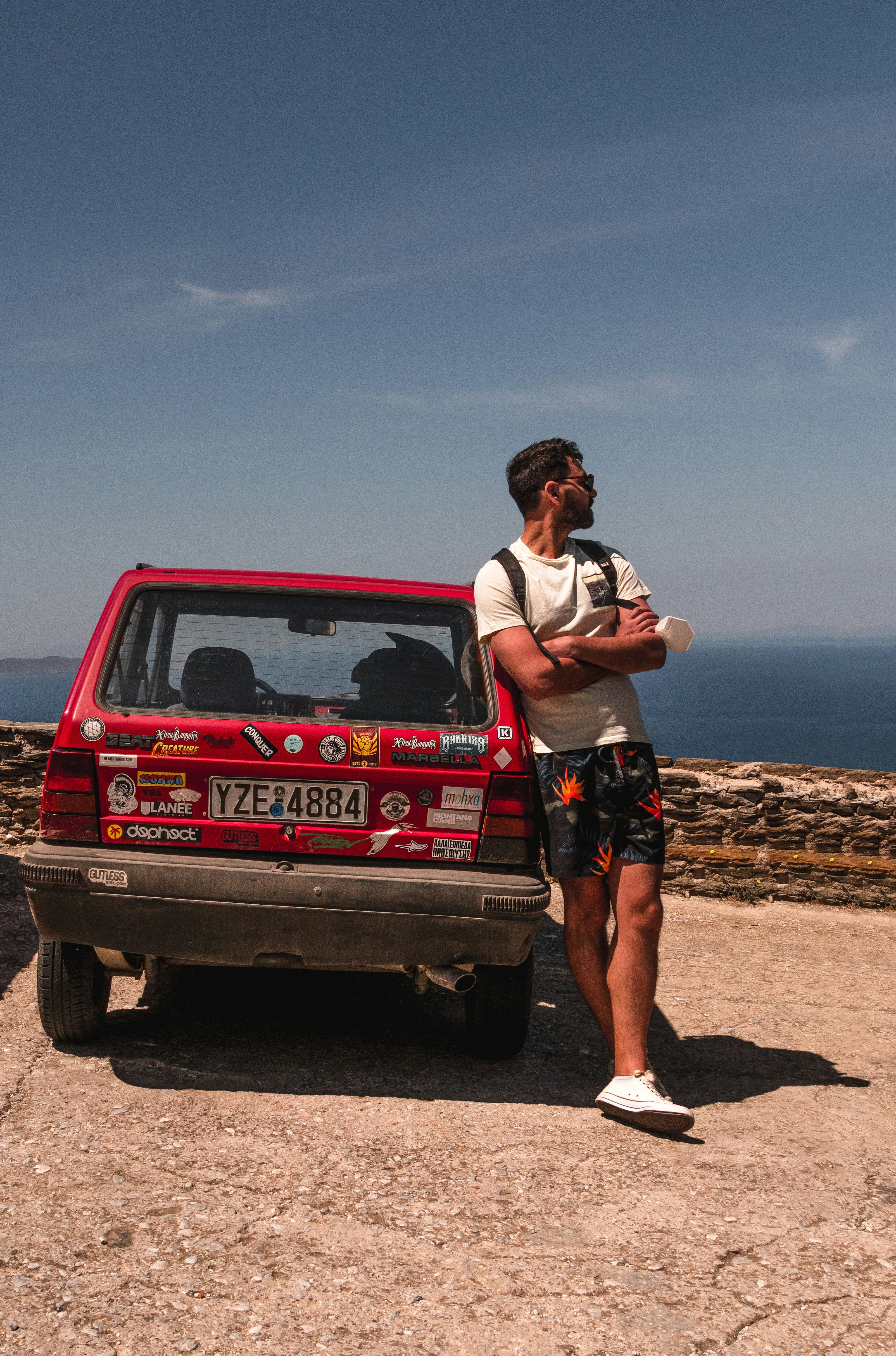 Cliffside Stance: Stickered Red Hatchback by the Sea