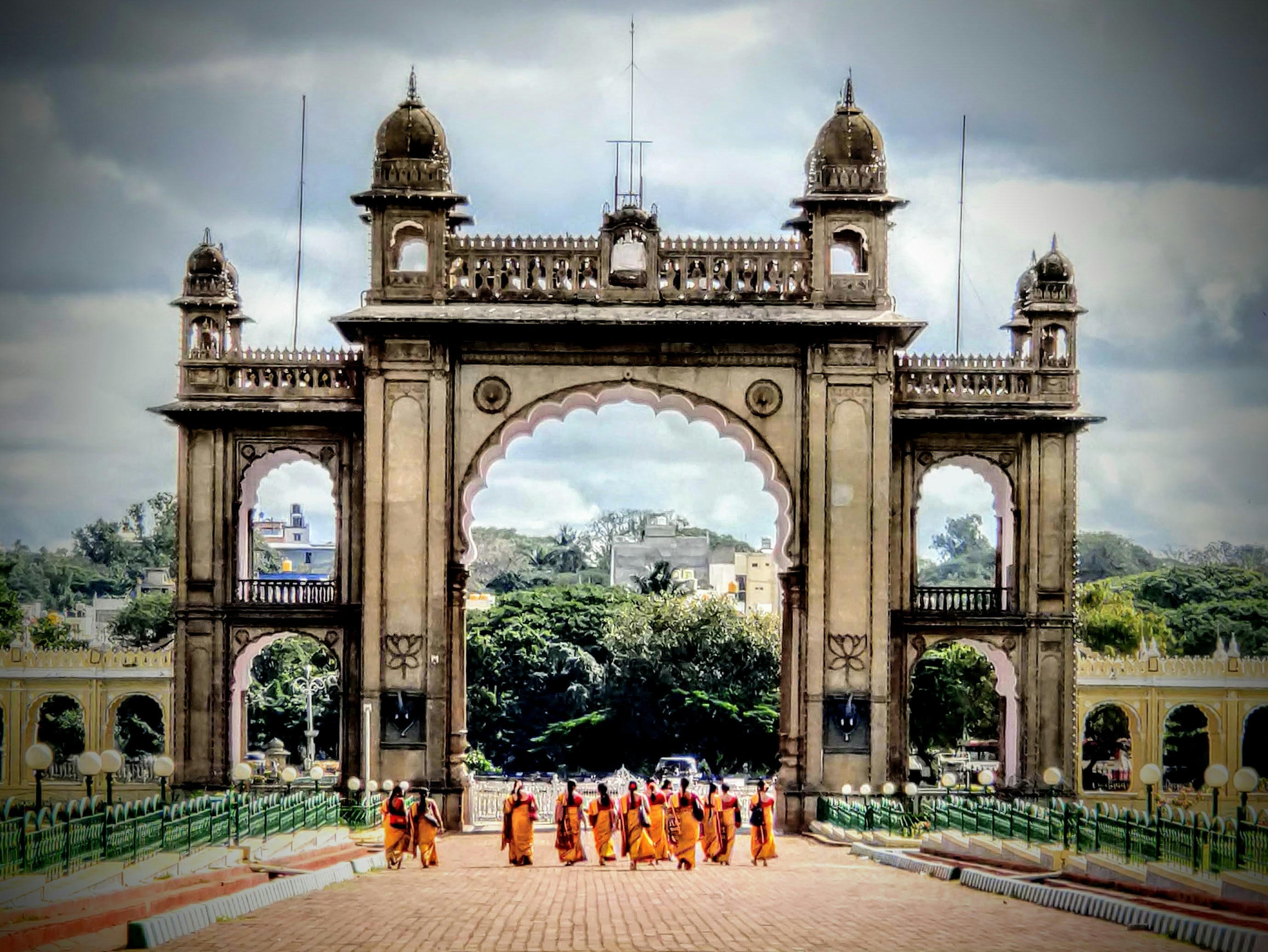 Monks in traditional attire walking beneath a grand archway, surrounded by lush greenery and historical architecture.
