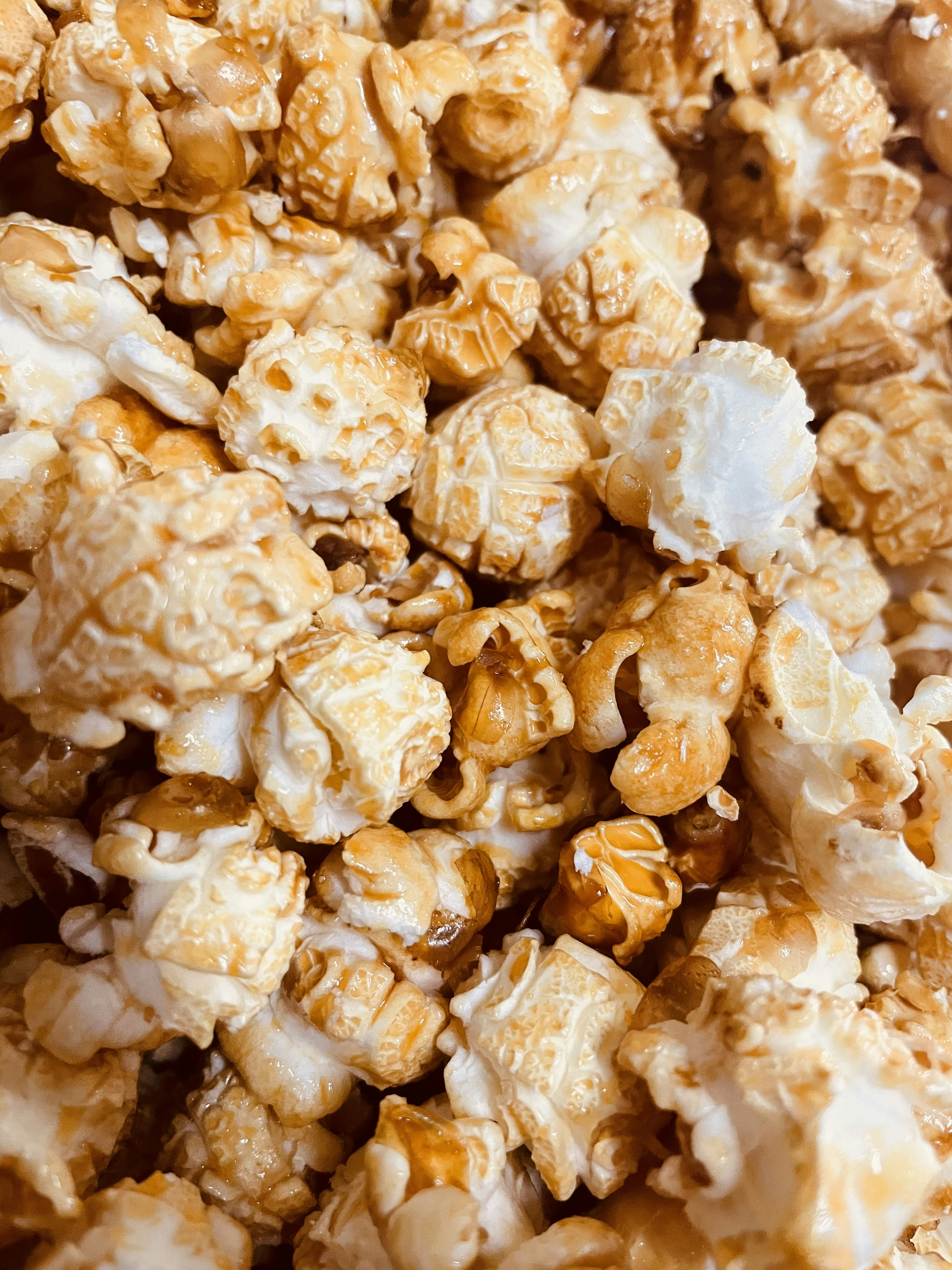 Close-up of caramel-coated popcorn, showcasing a variety of textures and colors. The golden hues and glossy finish highlight the sweet treat's appeal.