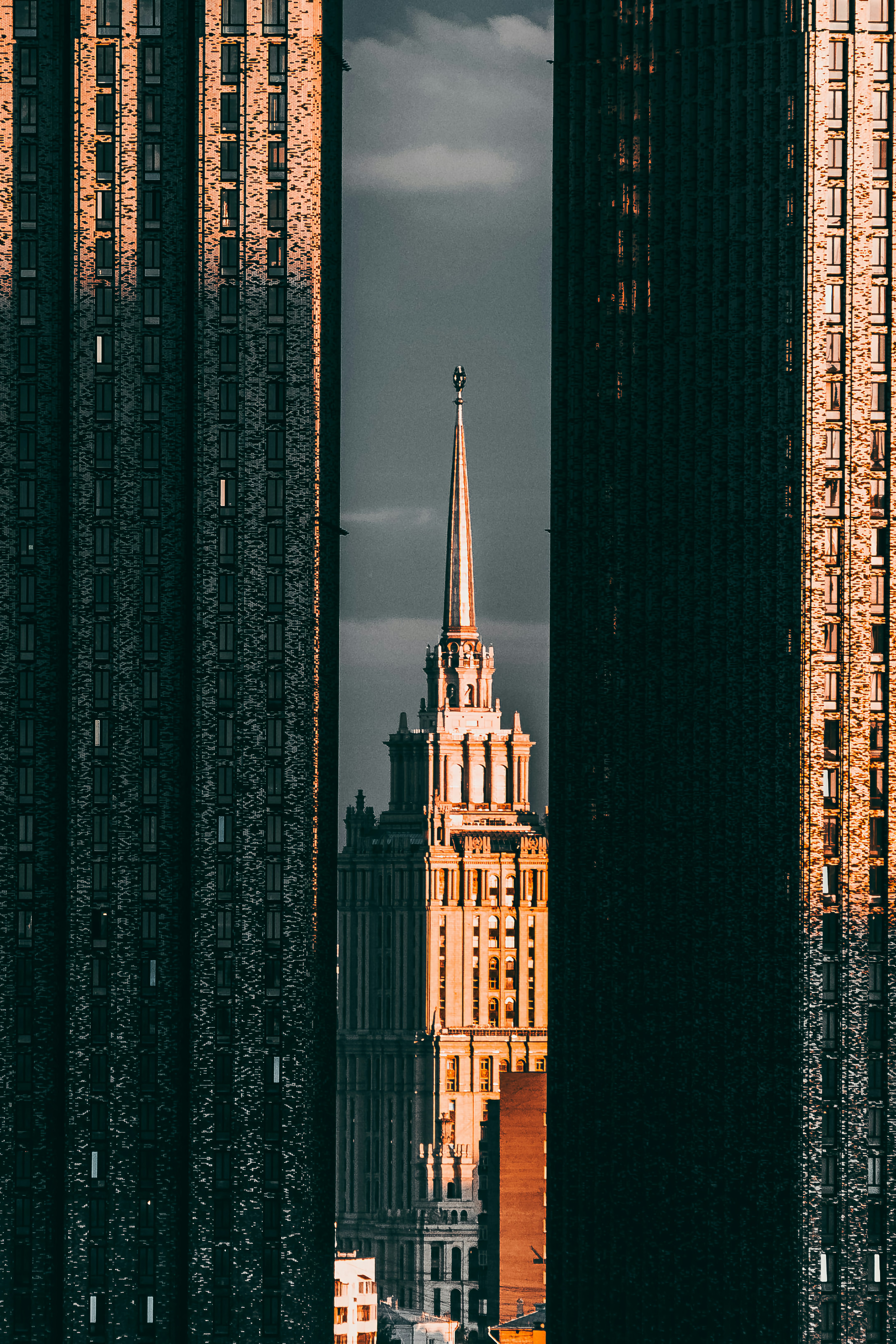 Illuminated historic building peeking between modern skyscrapers during sunset. The play of light and shadow creates a striking contrast.