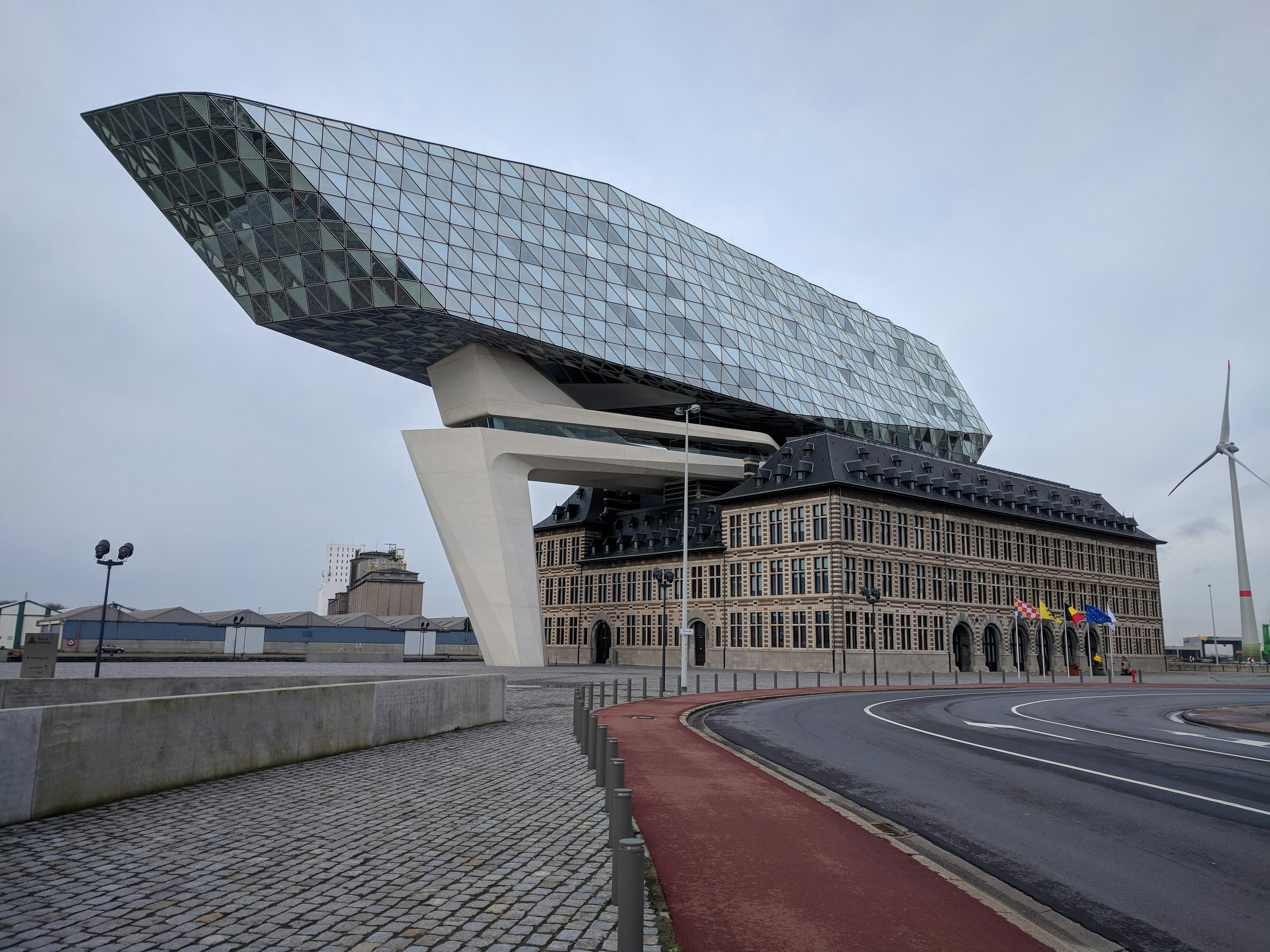 Futuristic glass building perched atop a historic structure under a cloudy sky.
