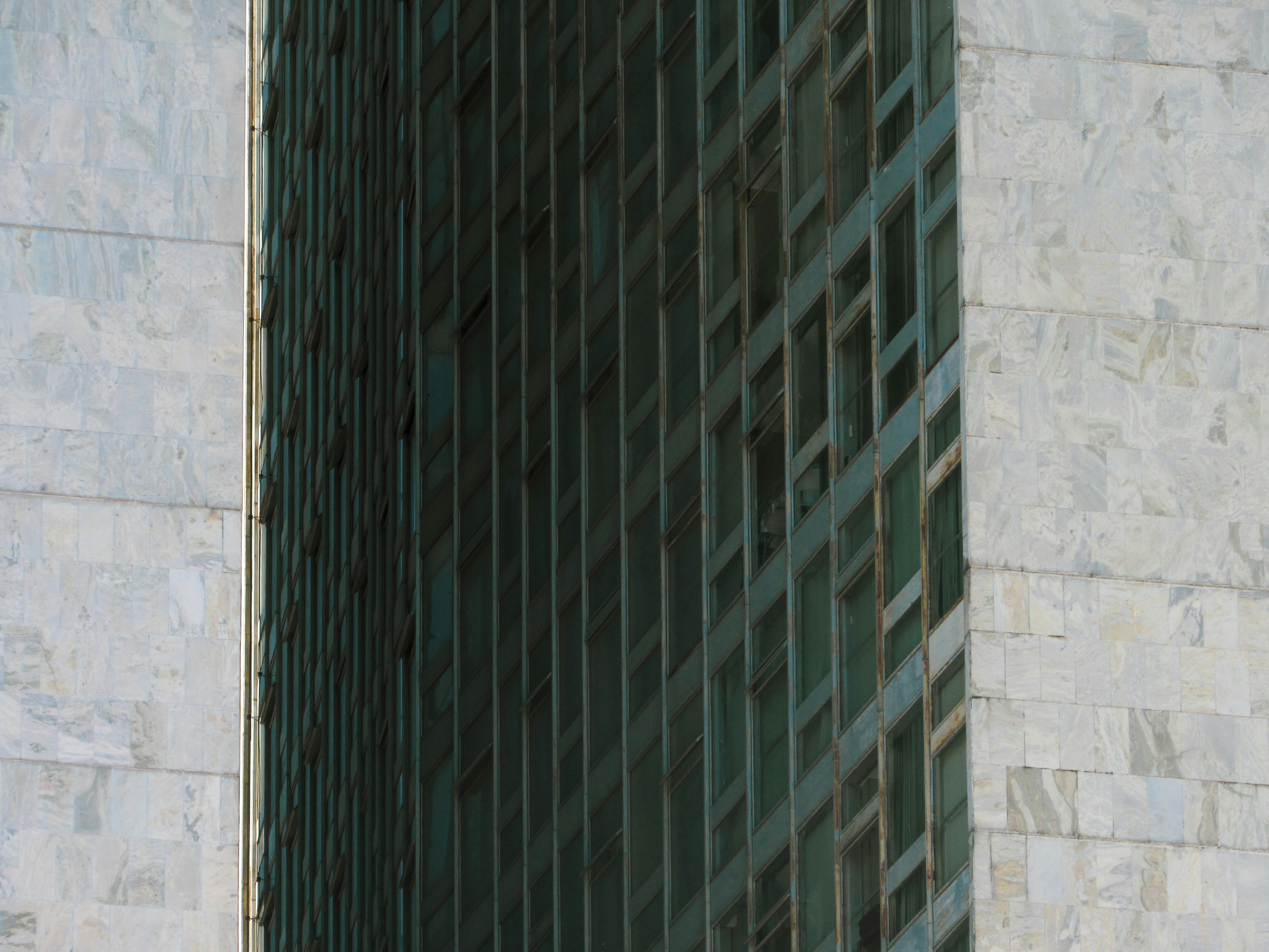 Architectural detail of a tall exterior with a dense grid of green-tinted windows set against light marble walls.