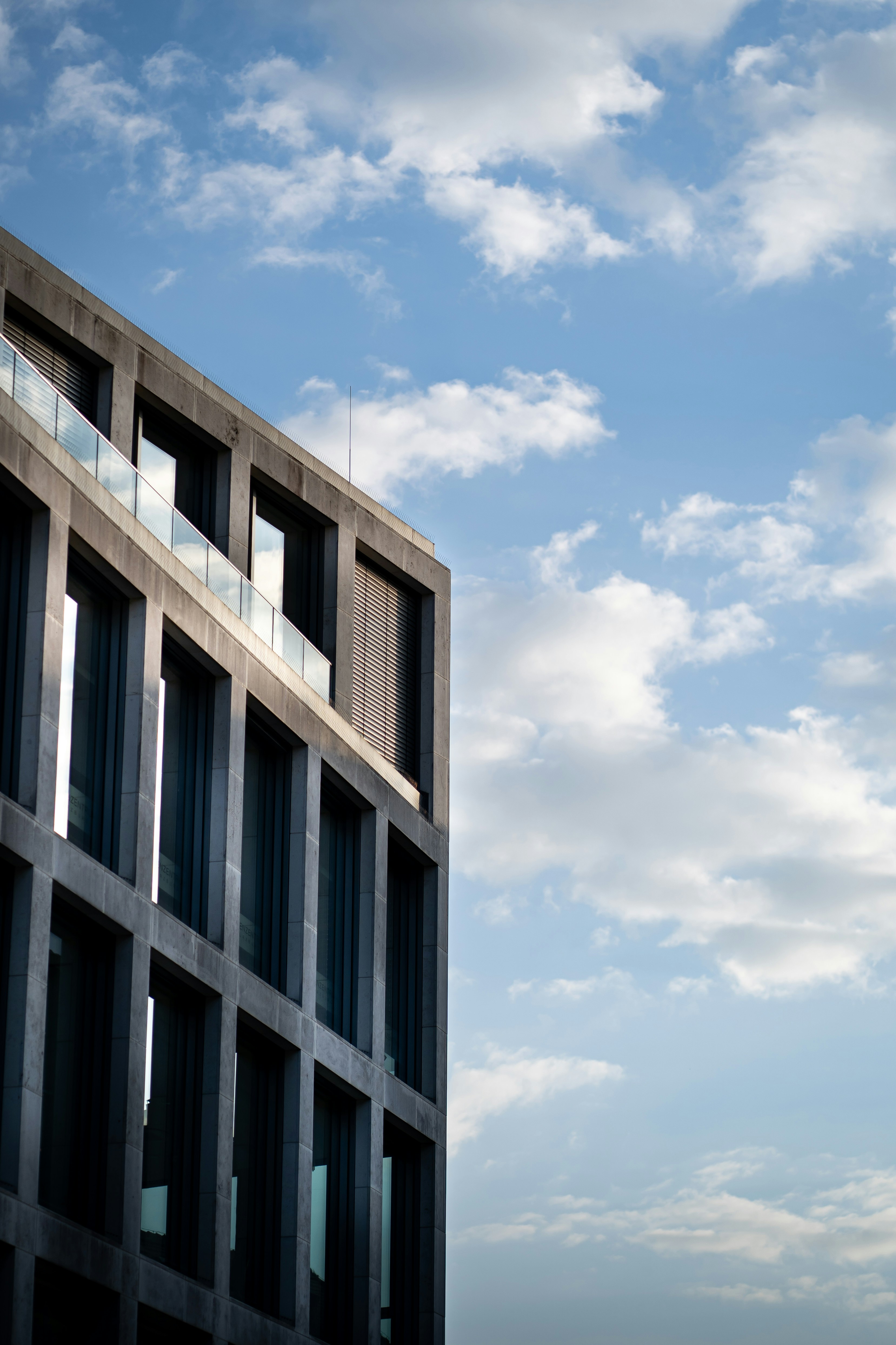 Modern building facade with large windows set against a backdrop of scattered clouds in a blue sky.