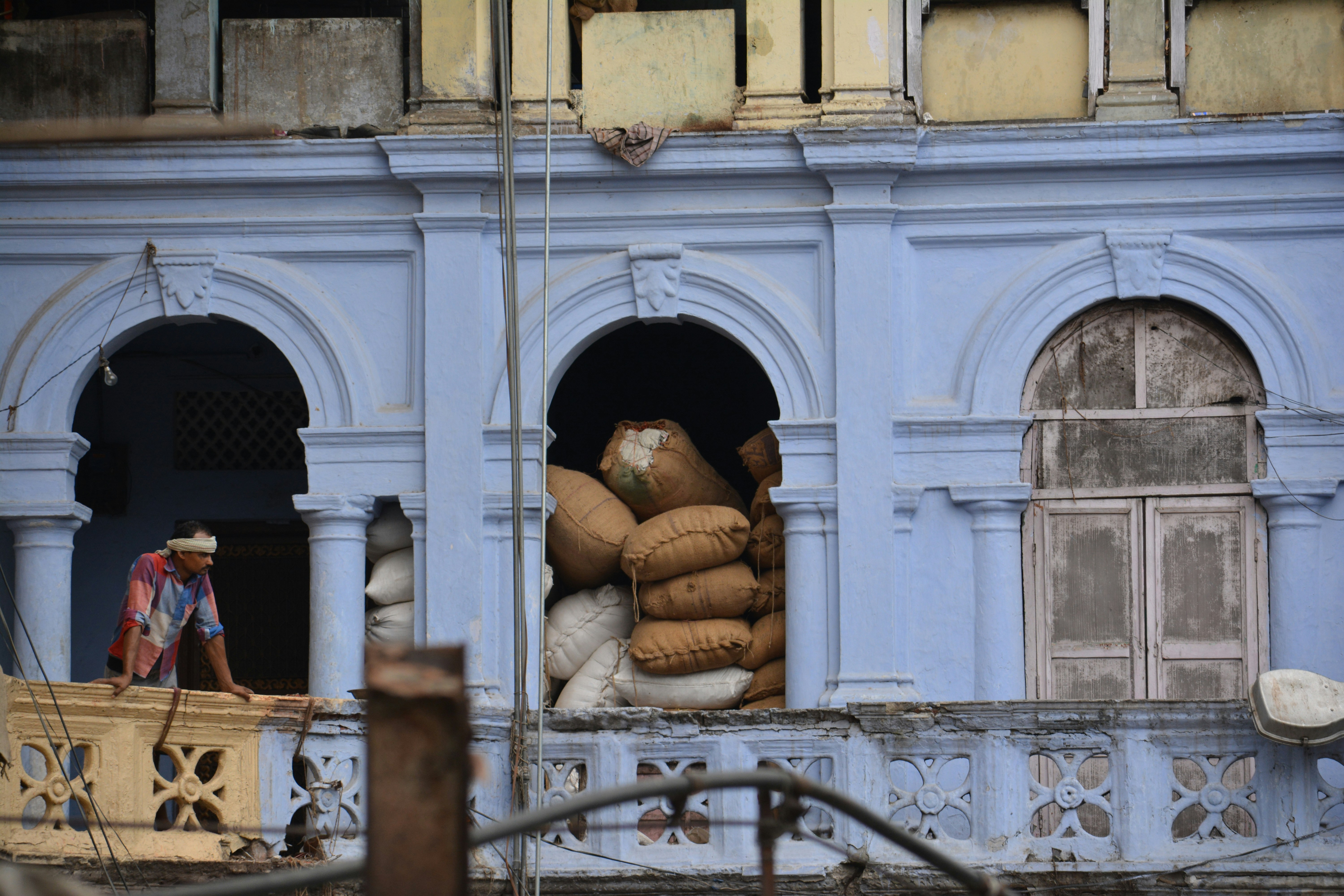 Blue Arches, Burlap Stacks: A Balcony Scene in Quiet Urban Light