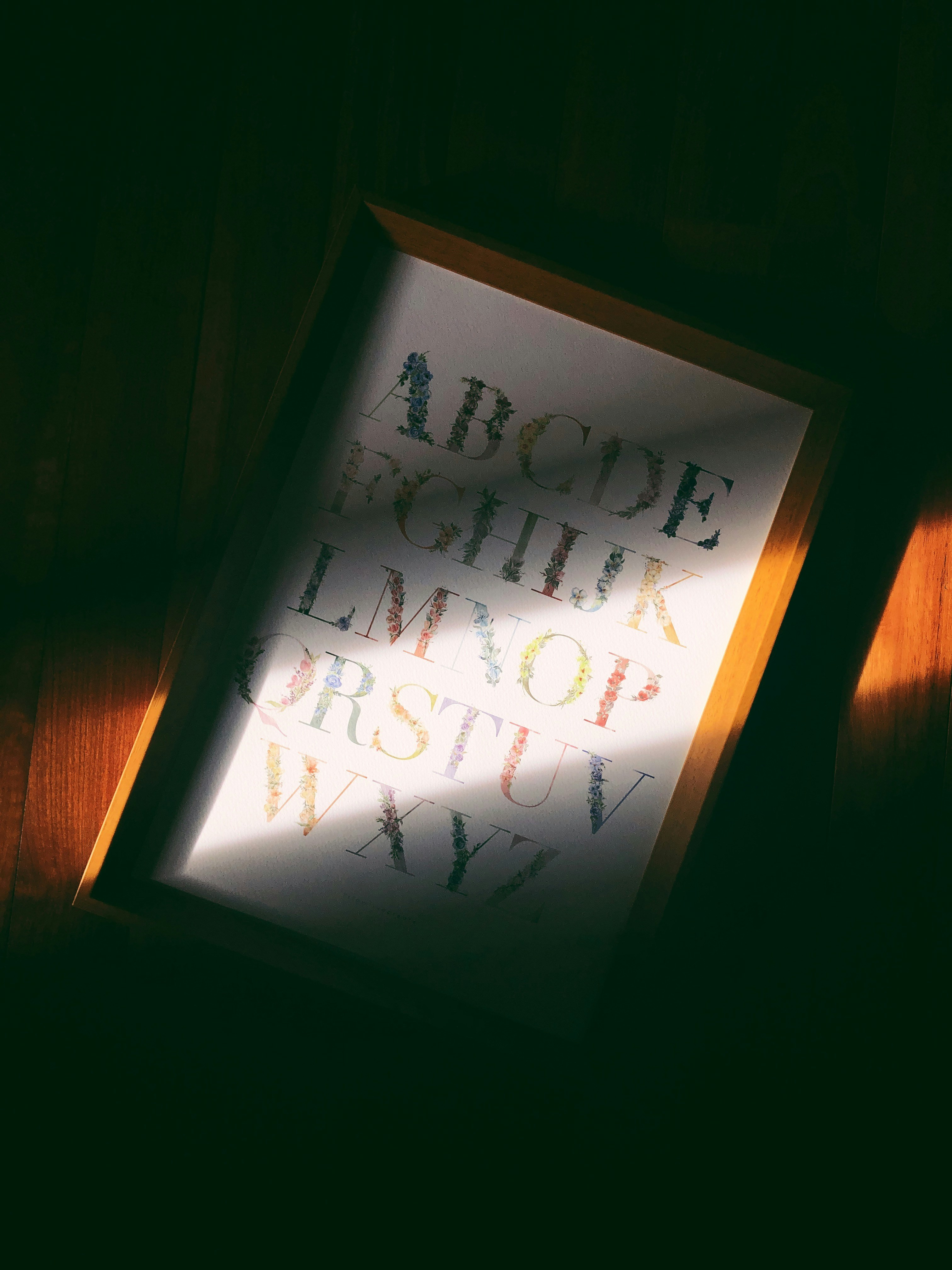 Tilted Alphabet: Warm Light Traces Multicolored Letters in a Framed Still Life