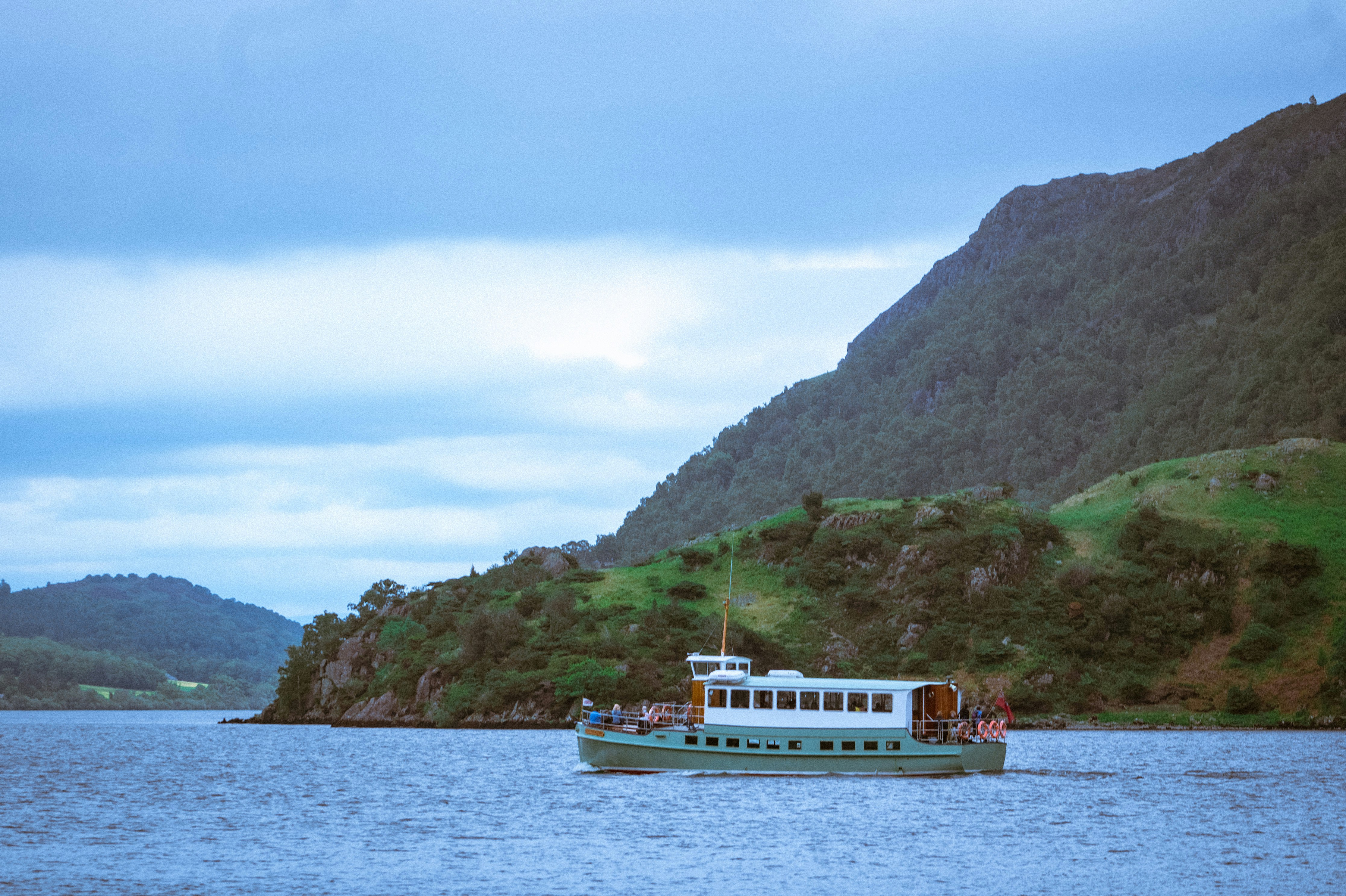 A vintage boat glides across a calm lake, framed by lush green hills and a moody sky, evoking a sense of peace and exploration.