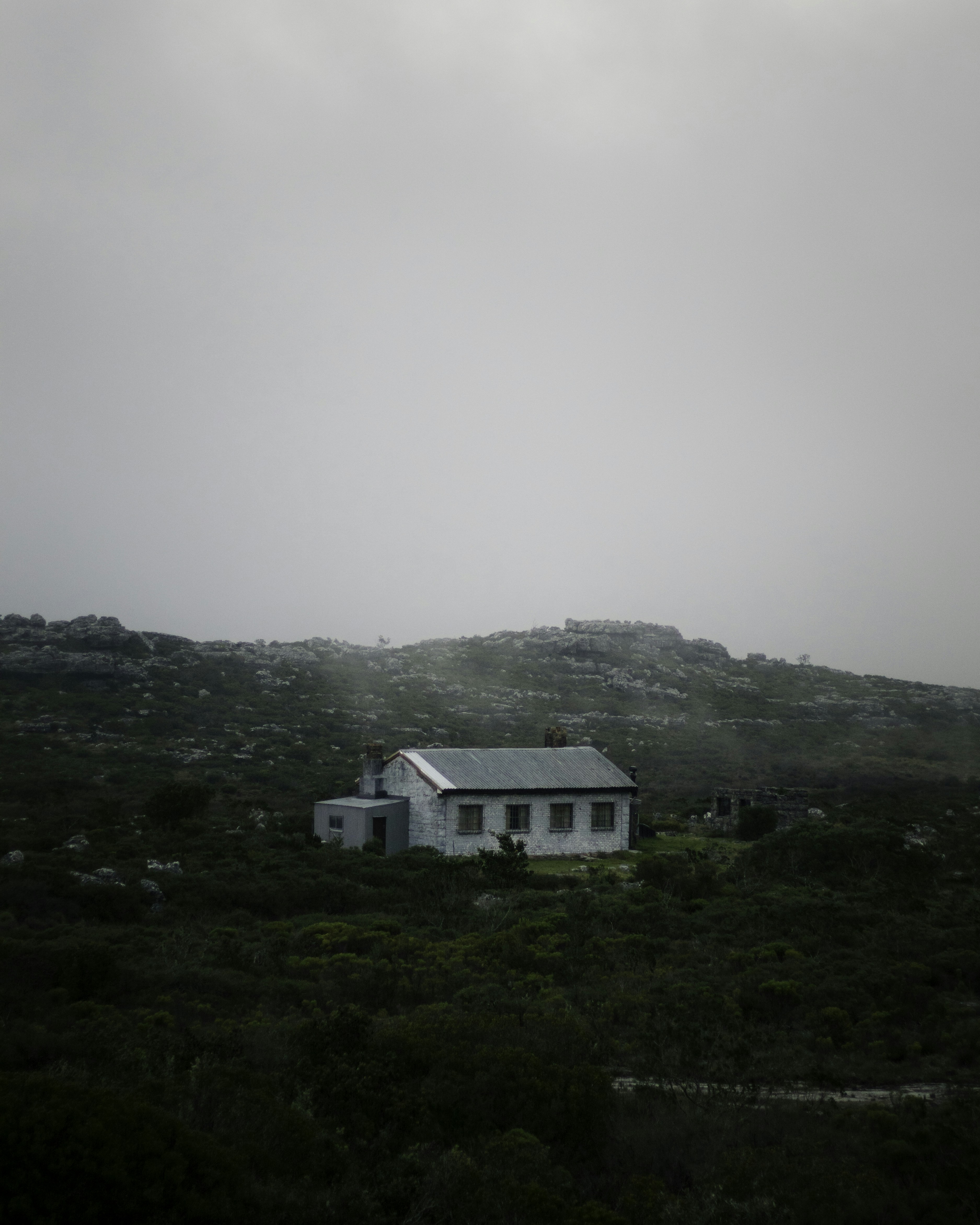 Isolated white house nestled in a misty landscape, surrounded by rocky hills and greenery.