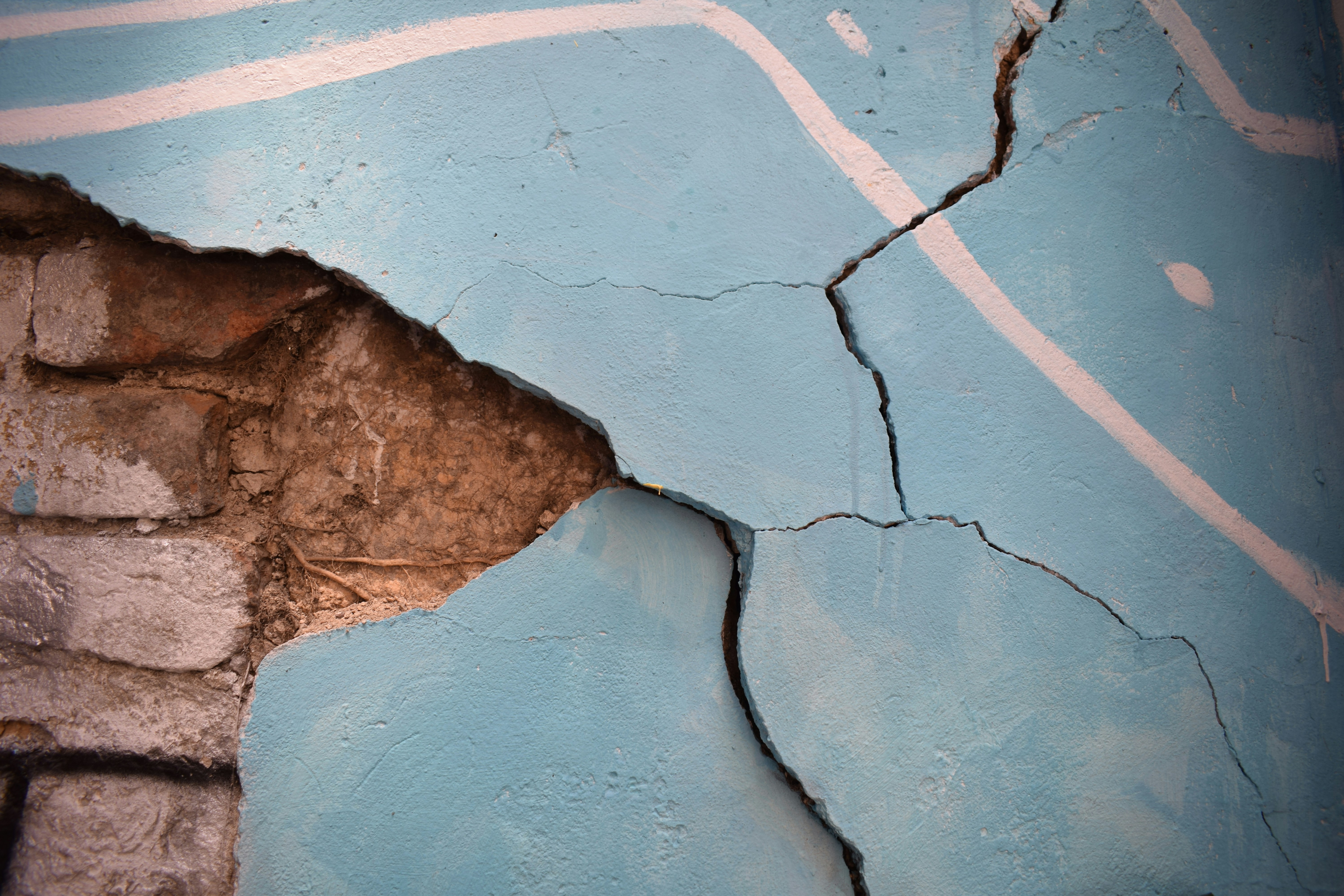 Cracked blue wall revealing a textured brick backdrop, highlighting the contrast between decay and color. The artwork's layers tell a story of time and resilience.