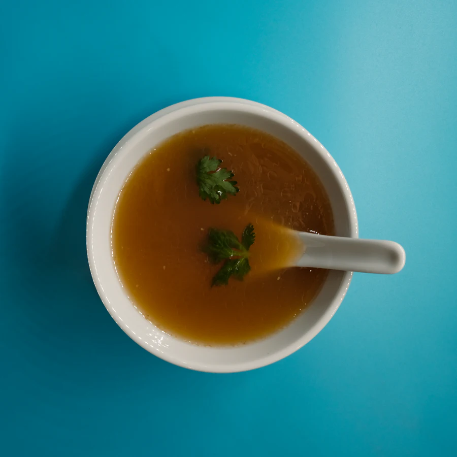 White bowl of golden soup on a bright blue table, garnished with cilantro and a spoon resting inside.