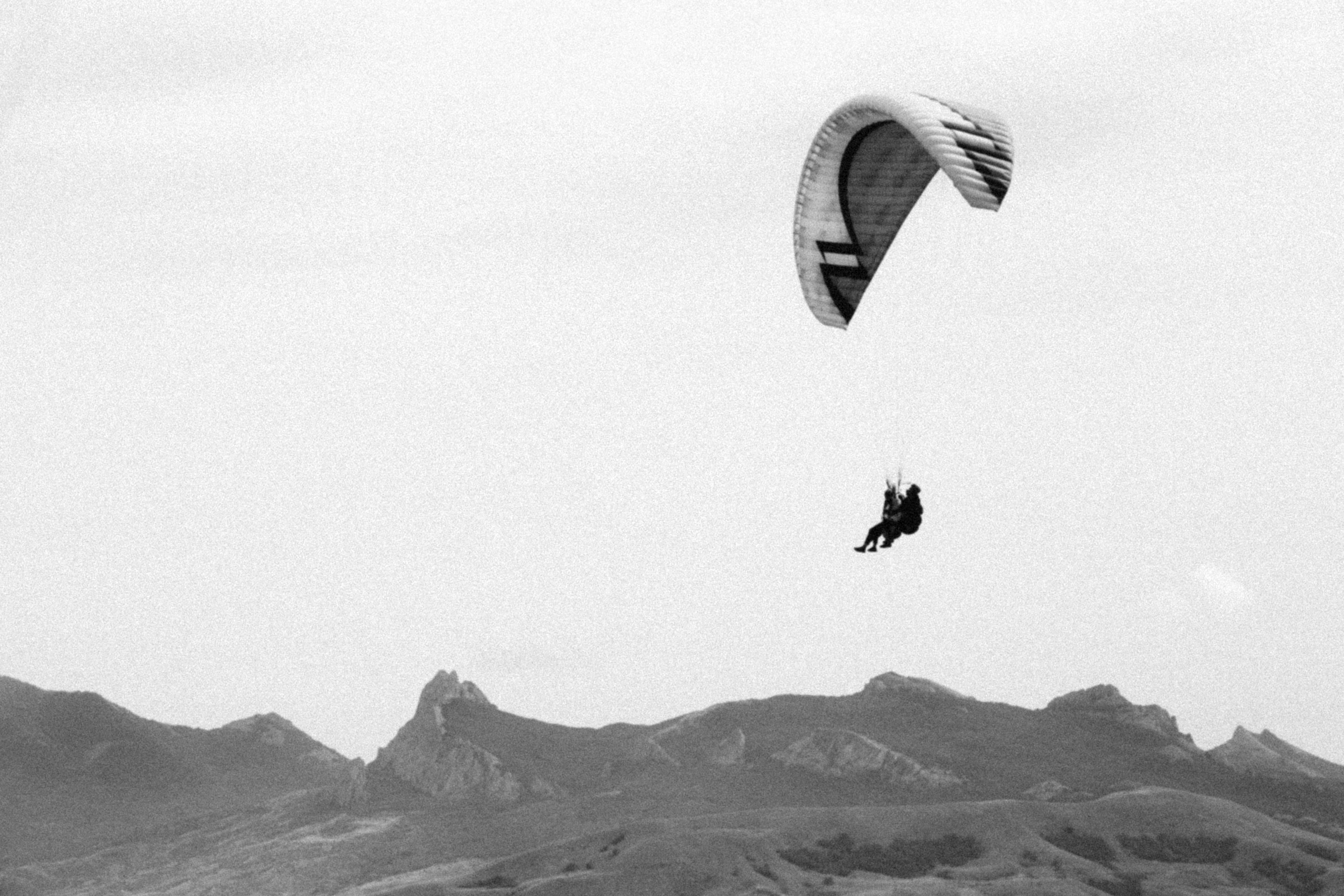 Soaring Silhouette: Paraglider Above Rugged Ridge