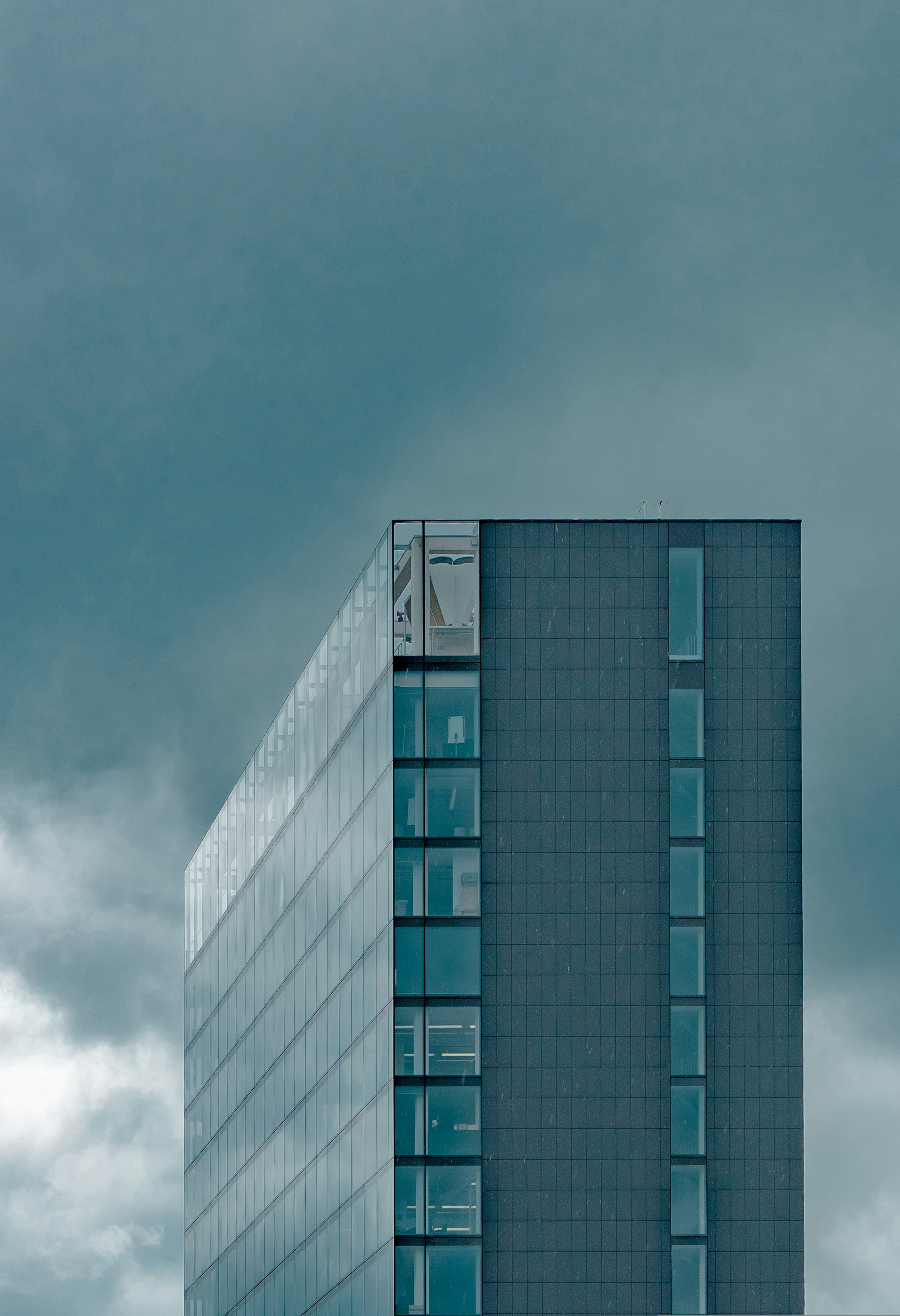 A sleek glass building stands against a moody sky, showcasing its modern design and reflective surfaces.