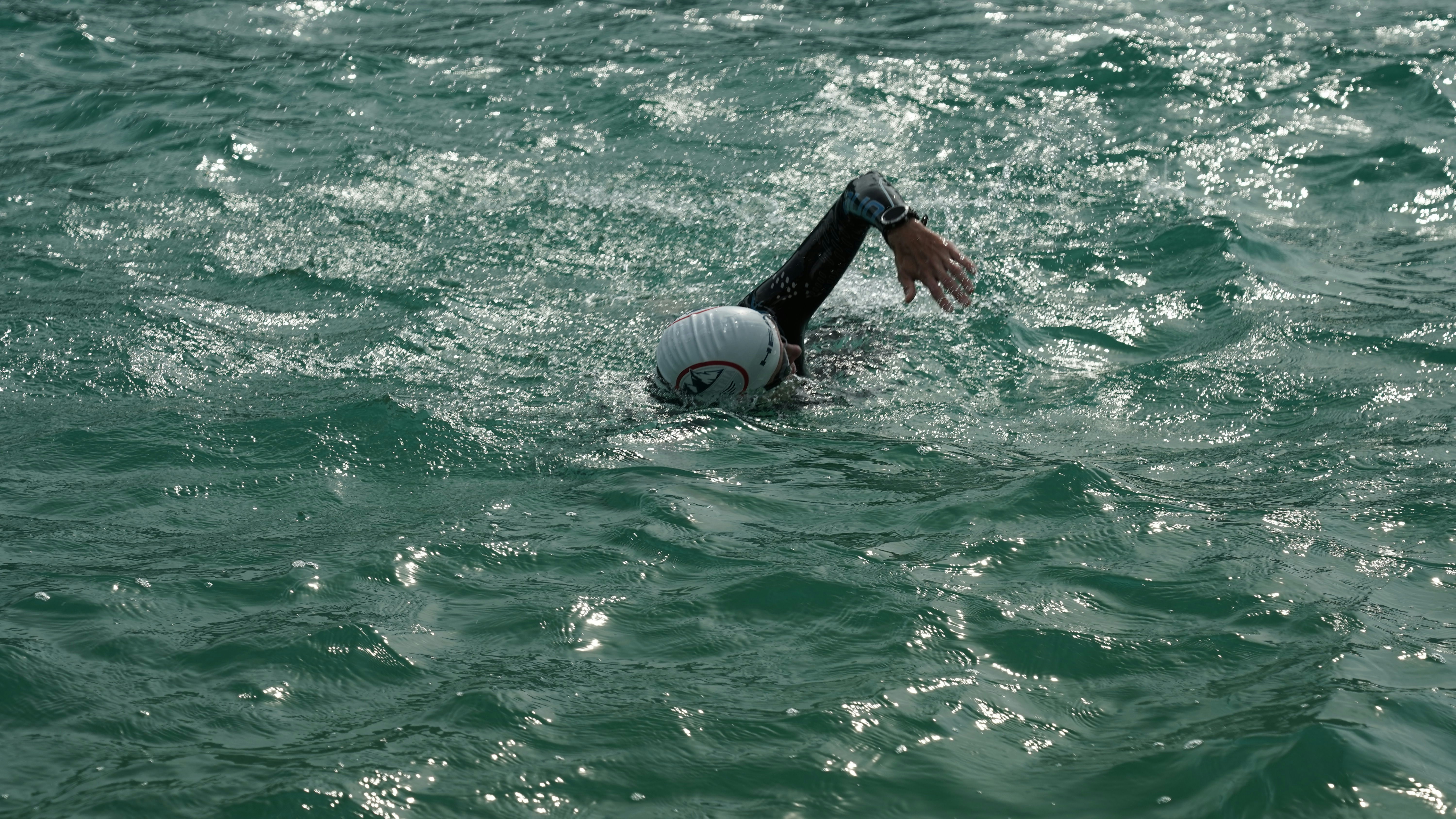 Swimmer in a black wetsuit navigates through turquoise waters, showcasing the blend of human endurance and nature's elements.