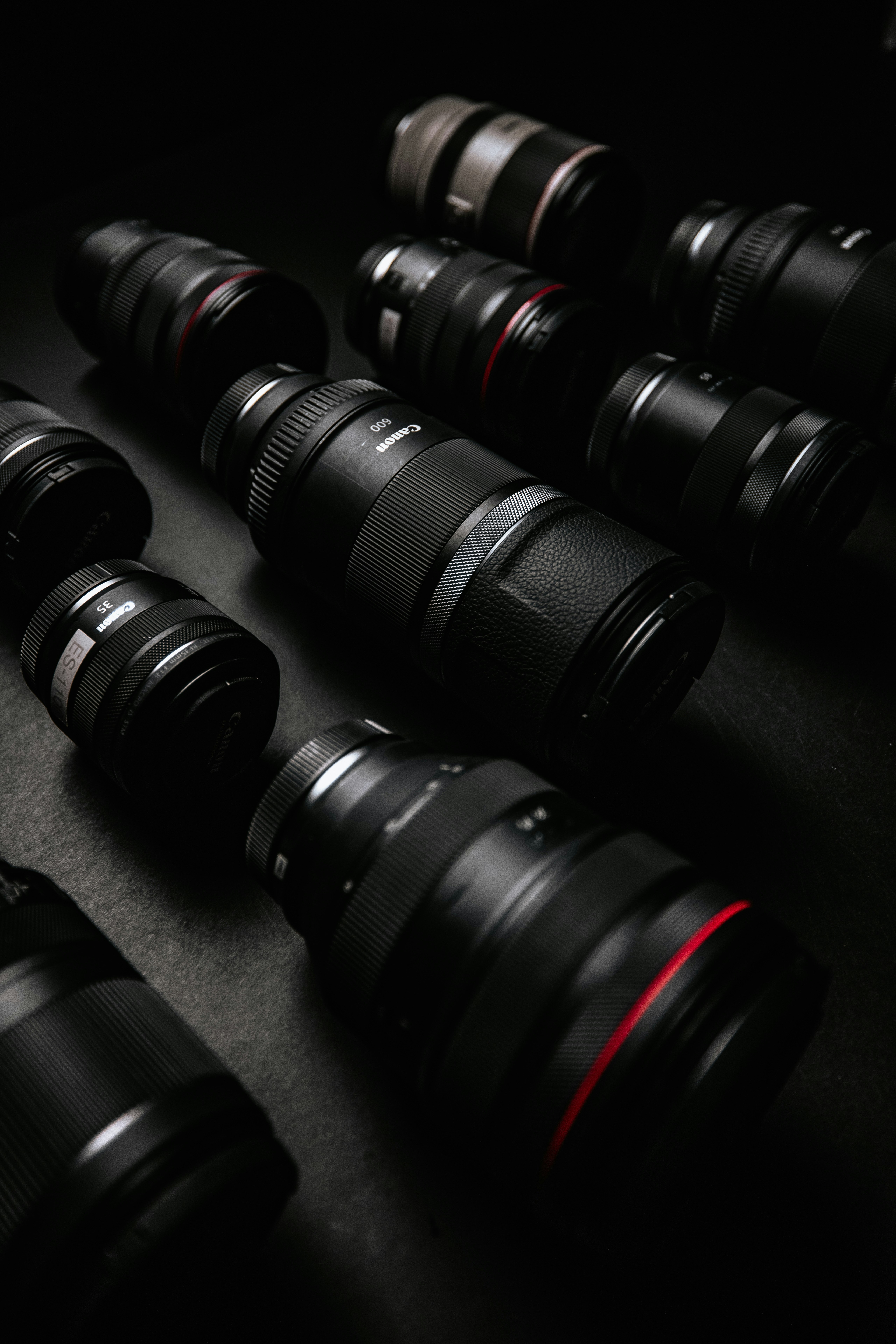 Array of various Canon camera lenses arranged artistically on a dark surface, showcasing their unique designs and features.