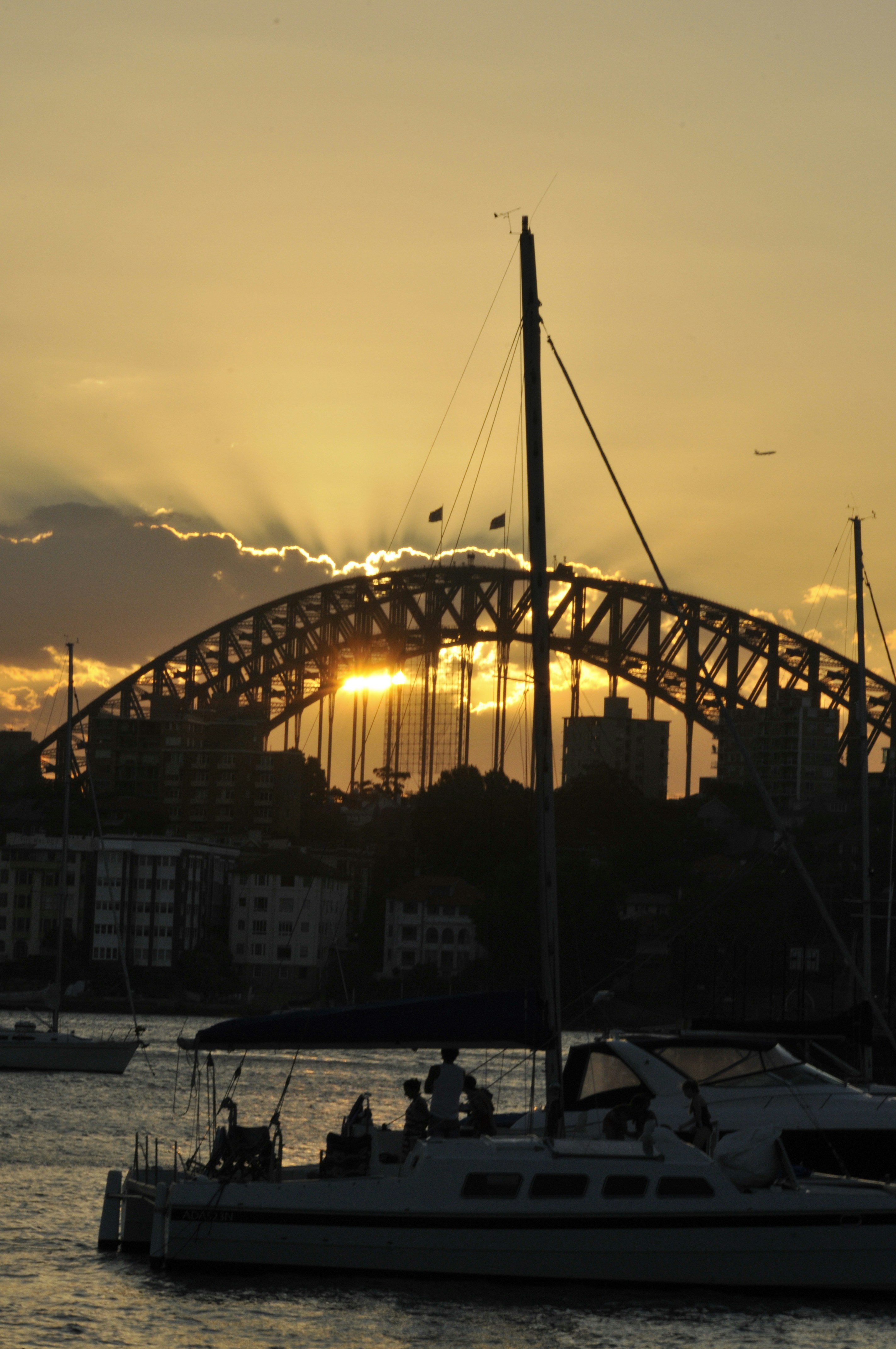 Sailboat anchored in foreground with the Sydney Harbour Bridge illuminated by the setting sun in the background.
