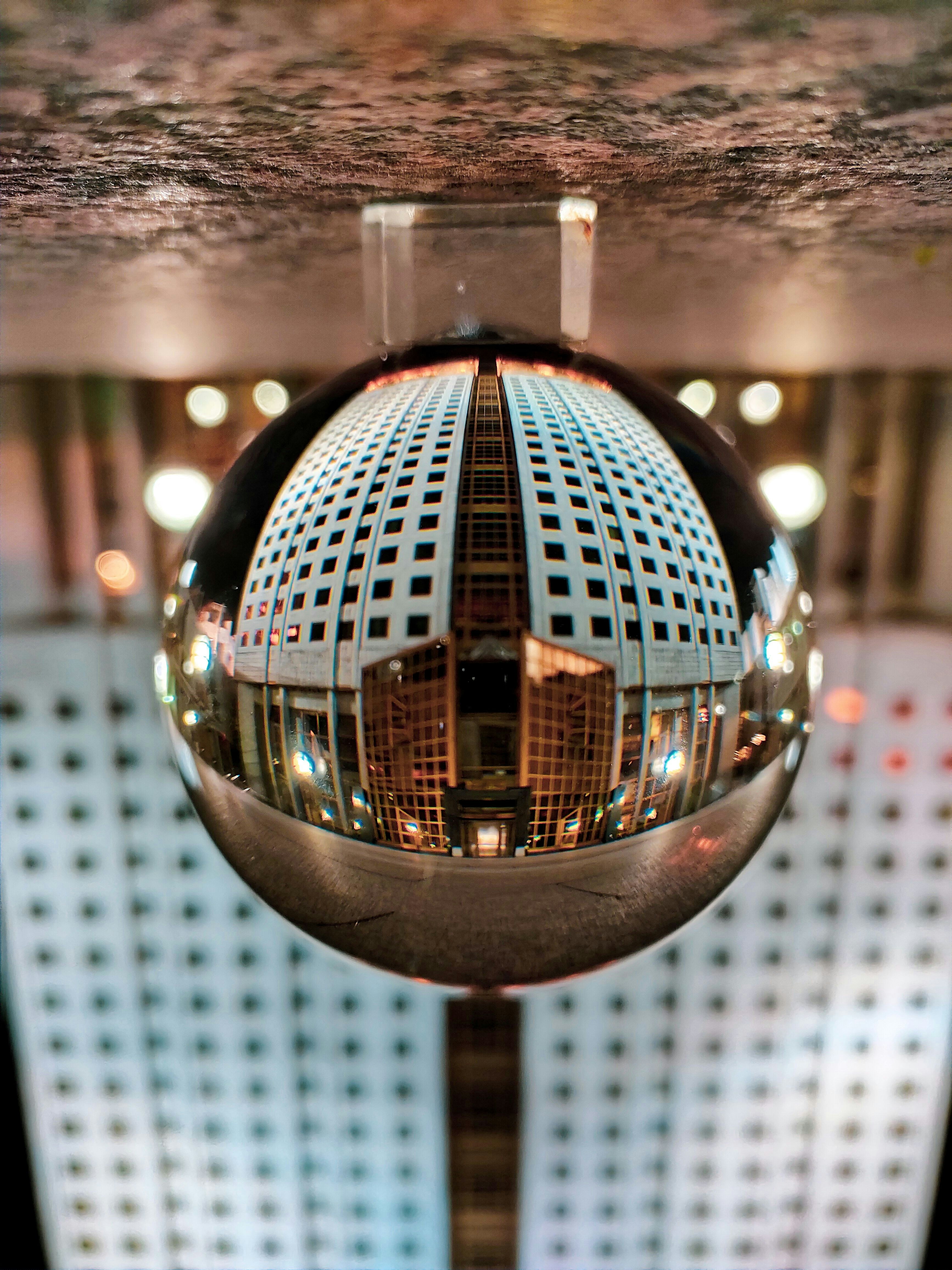 Reflective glass sphere displaying a modern building and ambient city lights, creating a unique perspective on urban architecture.