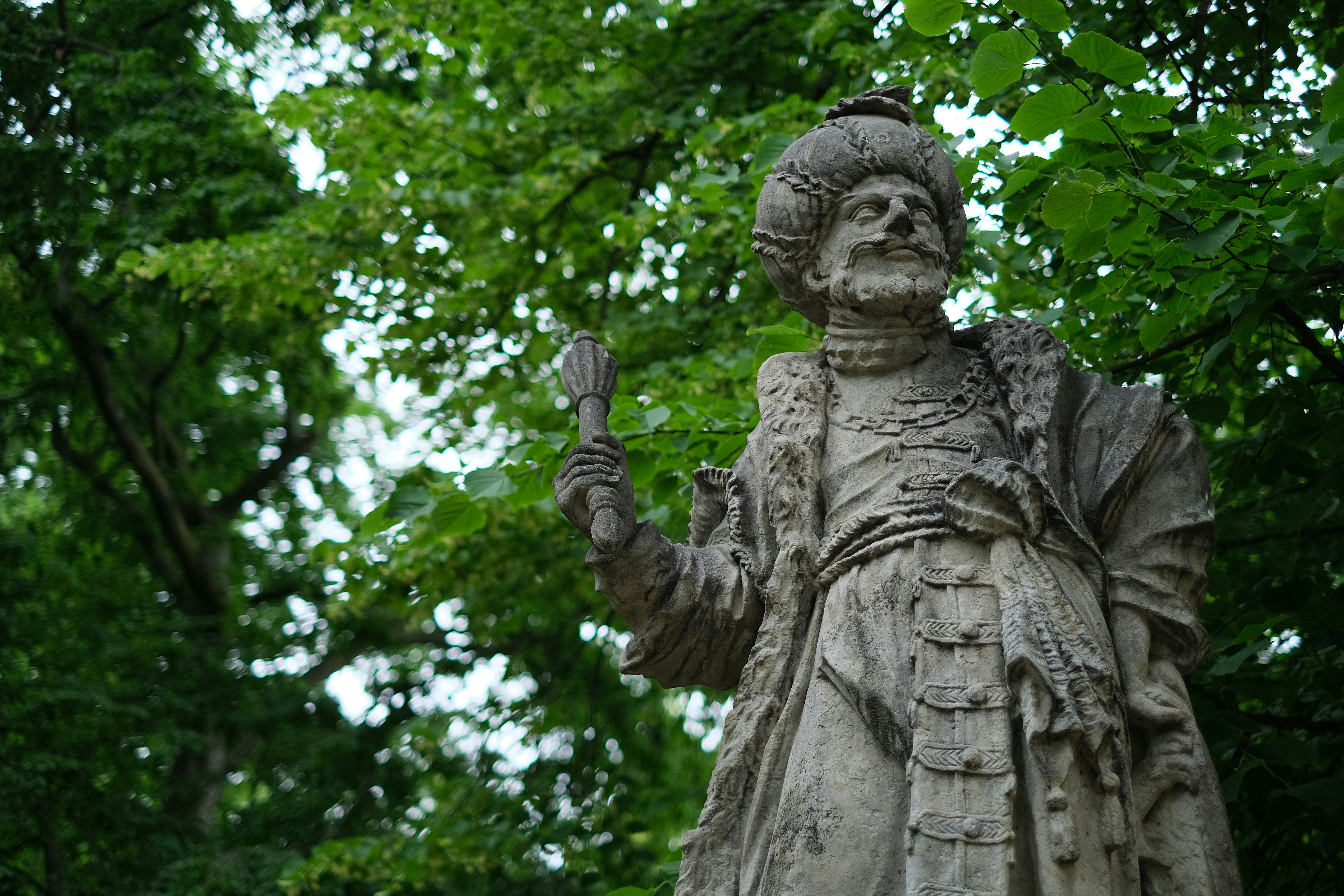 Ornate stone statue of a historical figure set against lush green trees.