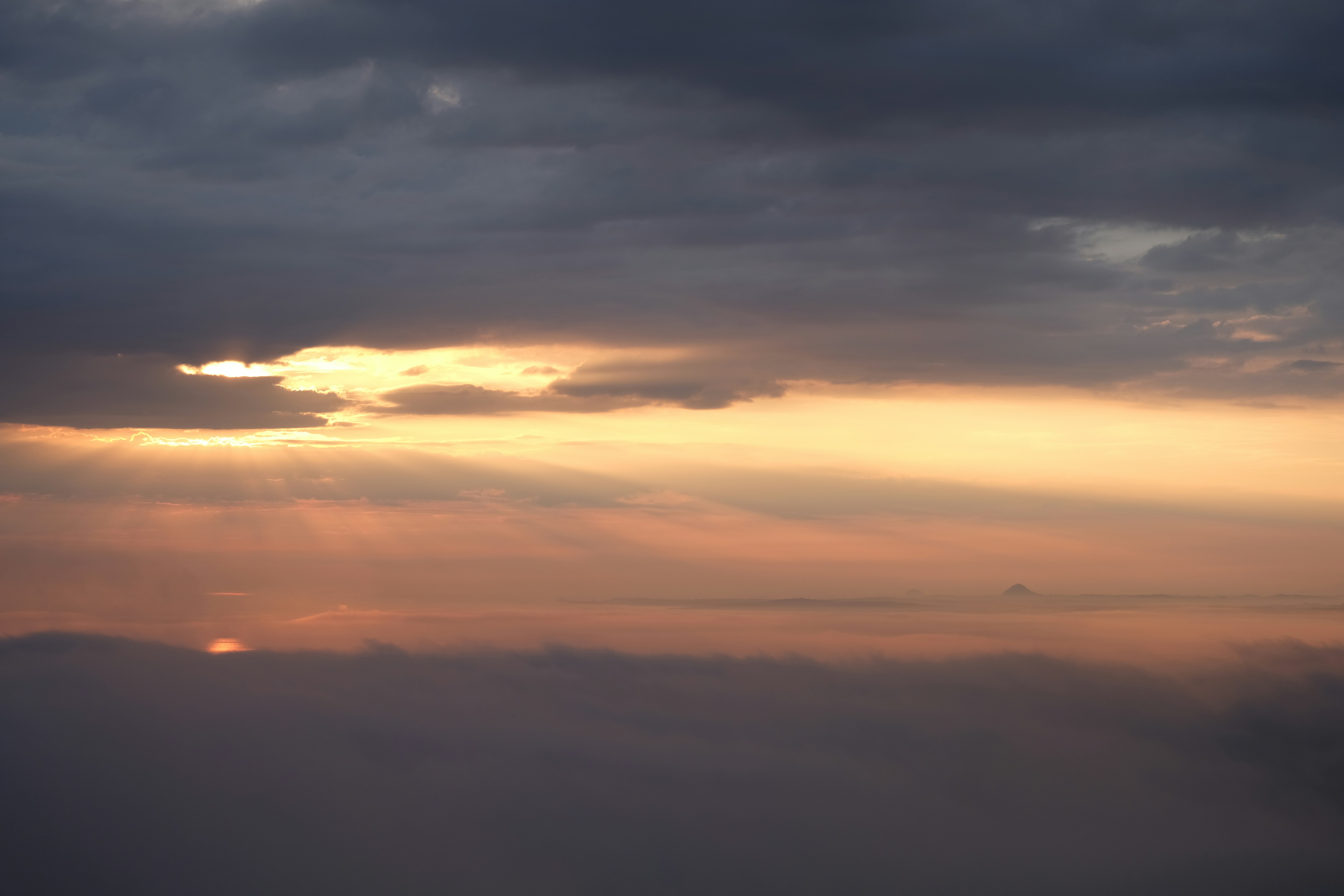 Soft sunlight breaking through clouds at sunrise, casting warm hues over a misty landscape.