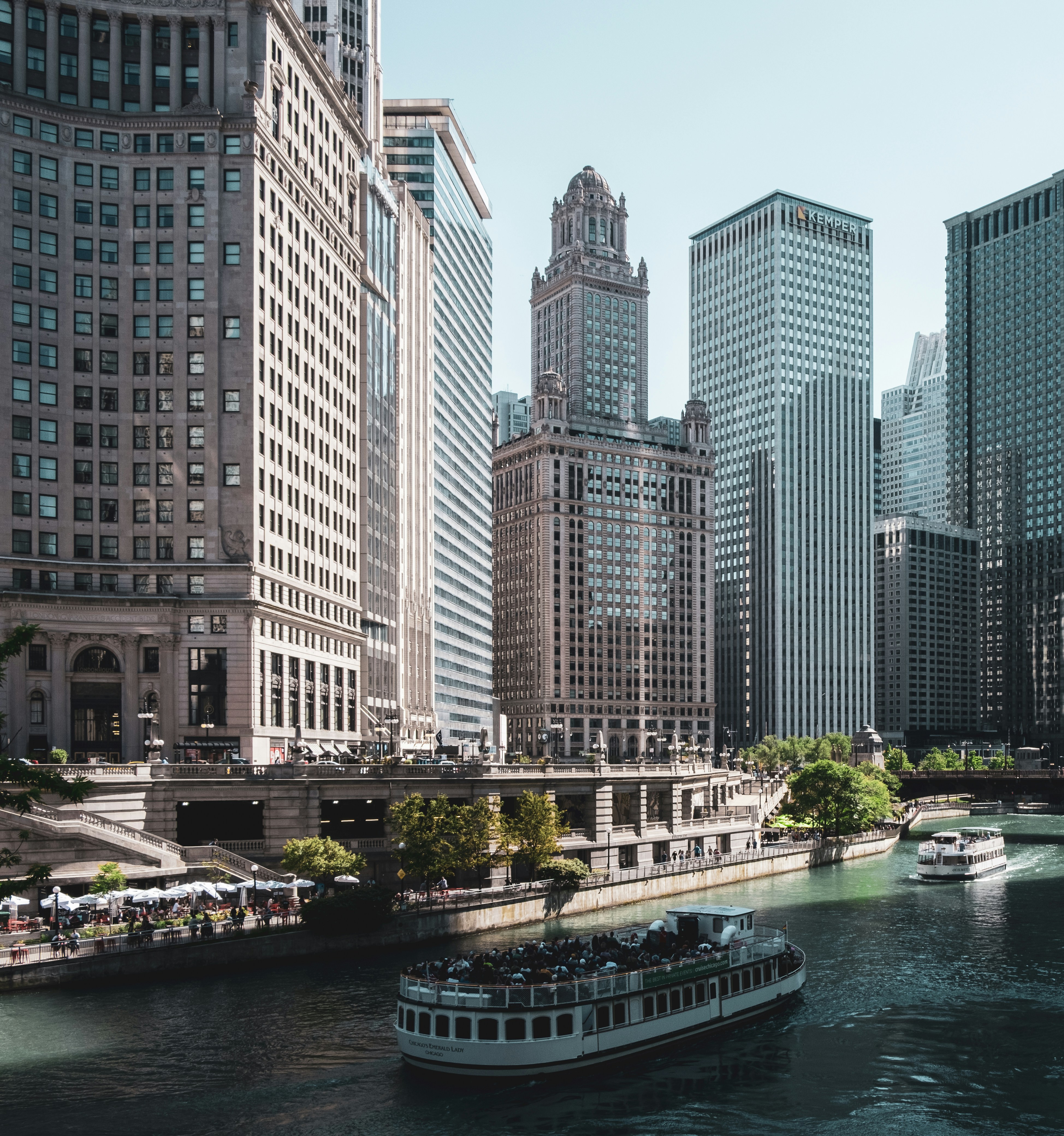 A vibrant cityscape featuring towering skyscrapers alongside a winding river, with boats gliding through the water. The scene captures the essence of urban life in a modern metropolis.