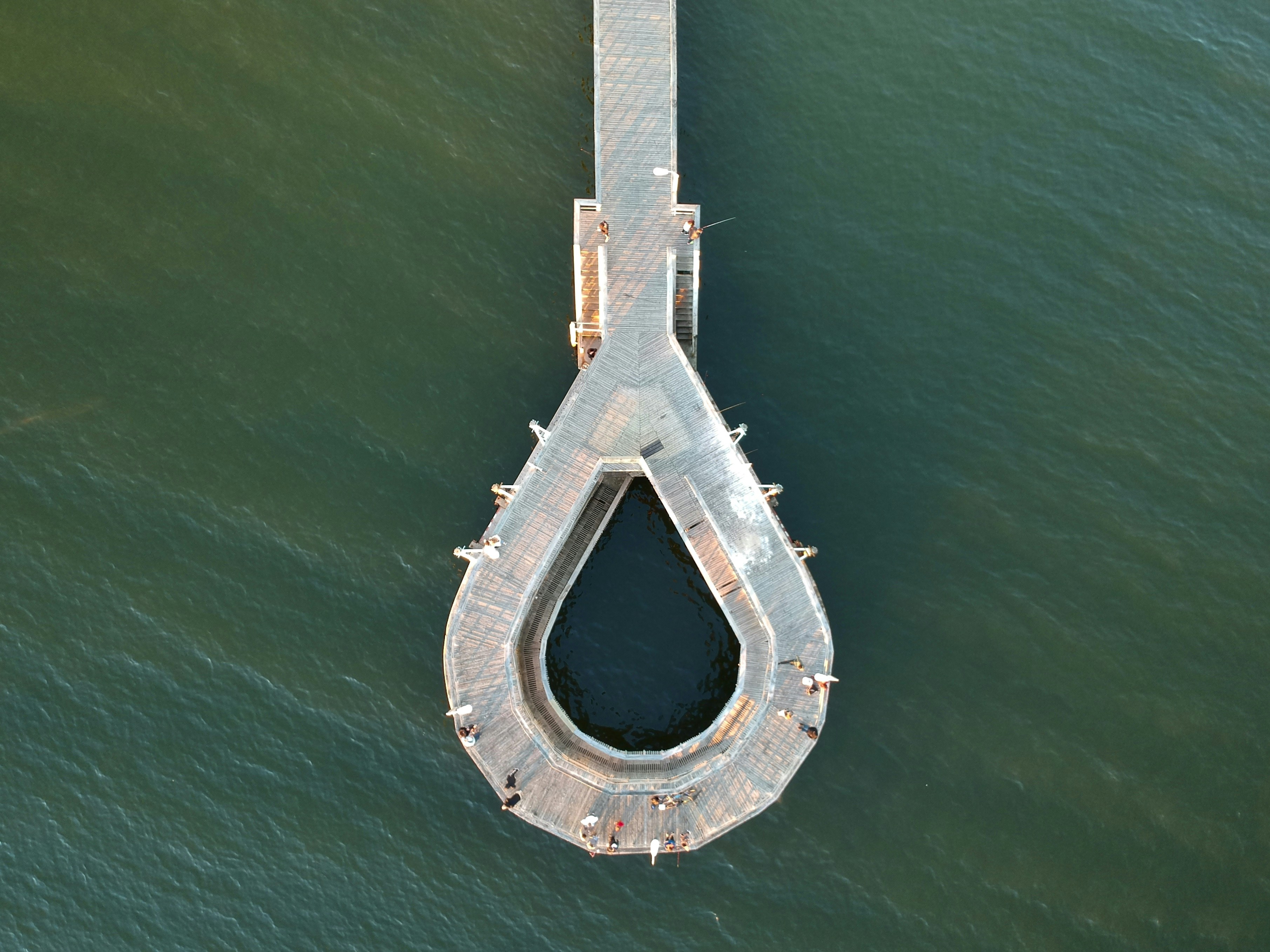 Aerial view of a pier shaped like a teardrop, surrounded by calm waters, highlighting the intricate design and serene environment.