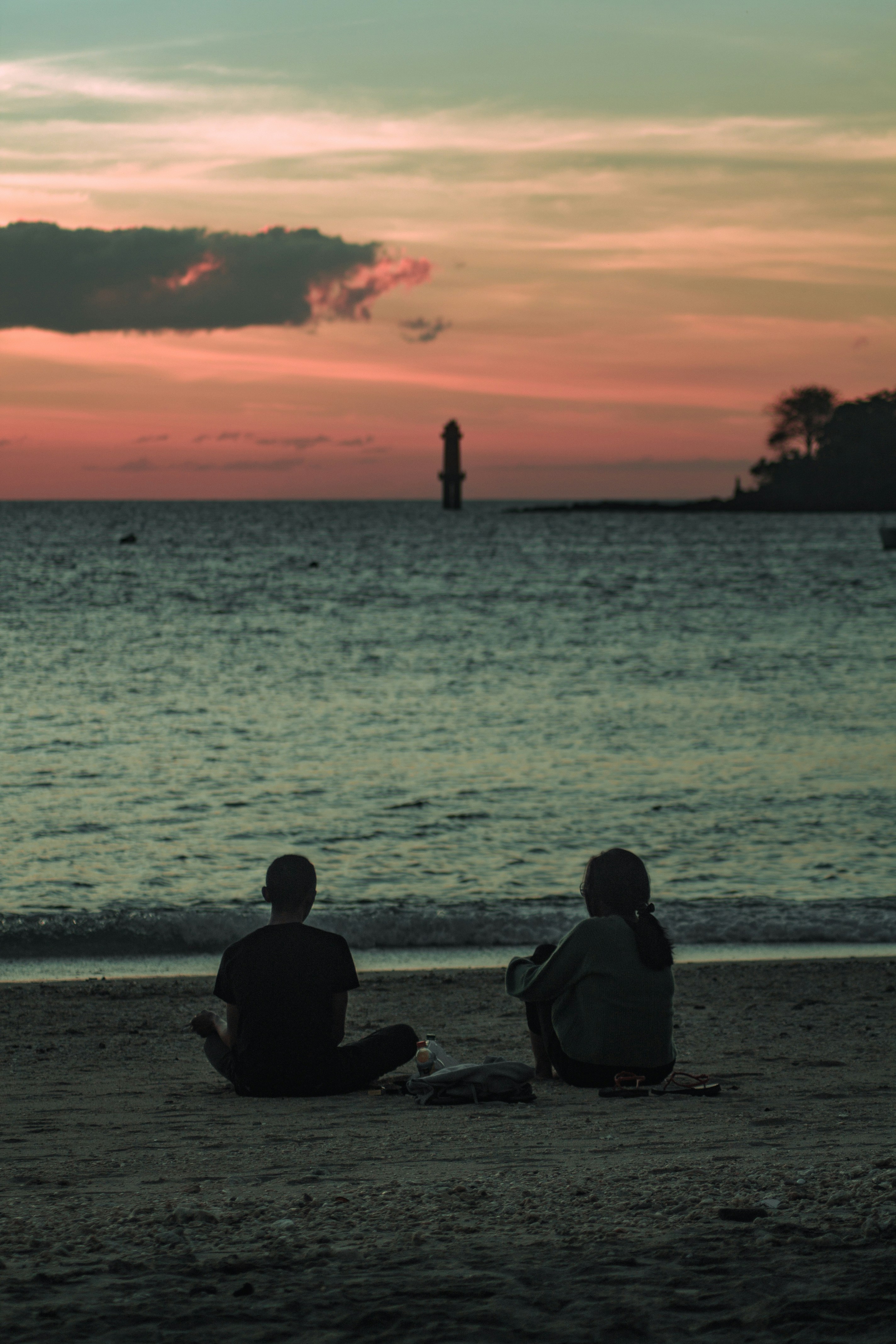 Silhouette de 2 personnes assises sur le rivage de la plage pendant le ...