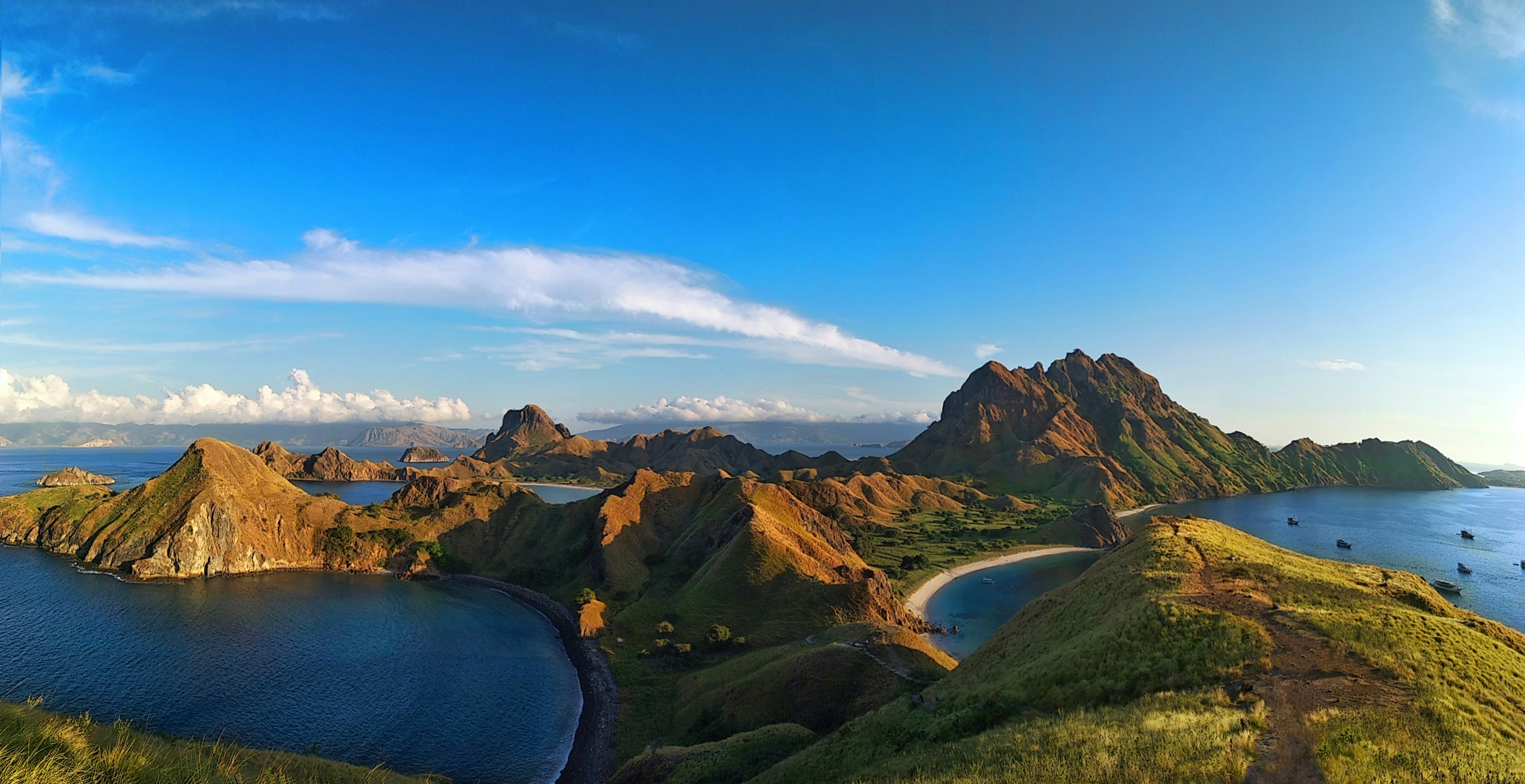 Vast panorama showcasing the rugged hills and tranquil waters of Komodo Island, with a winding path leading towards the horizon.