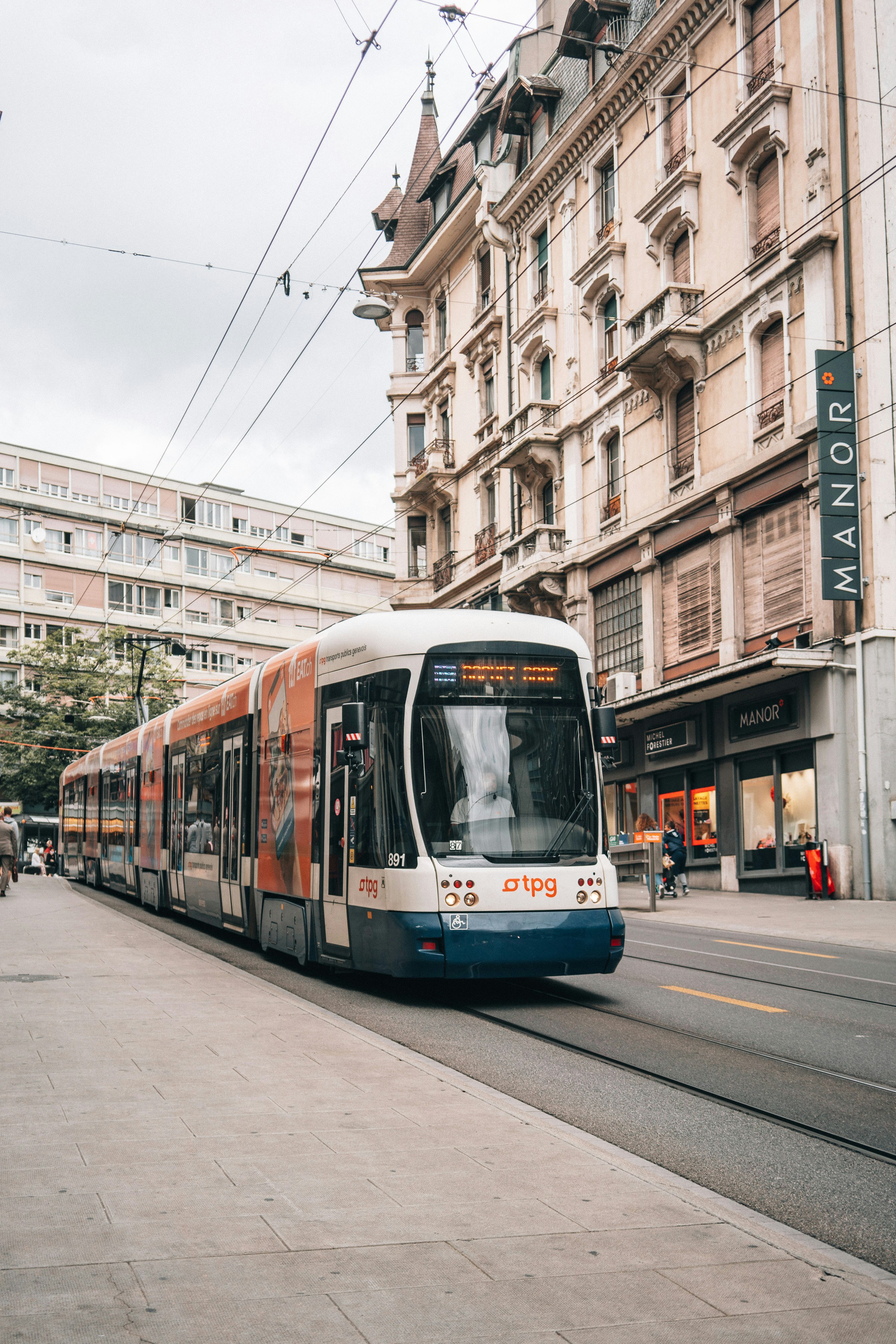 Tram navigating through a bustling city street, flanked by historic architecture and modern storefronts.