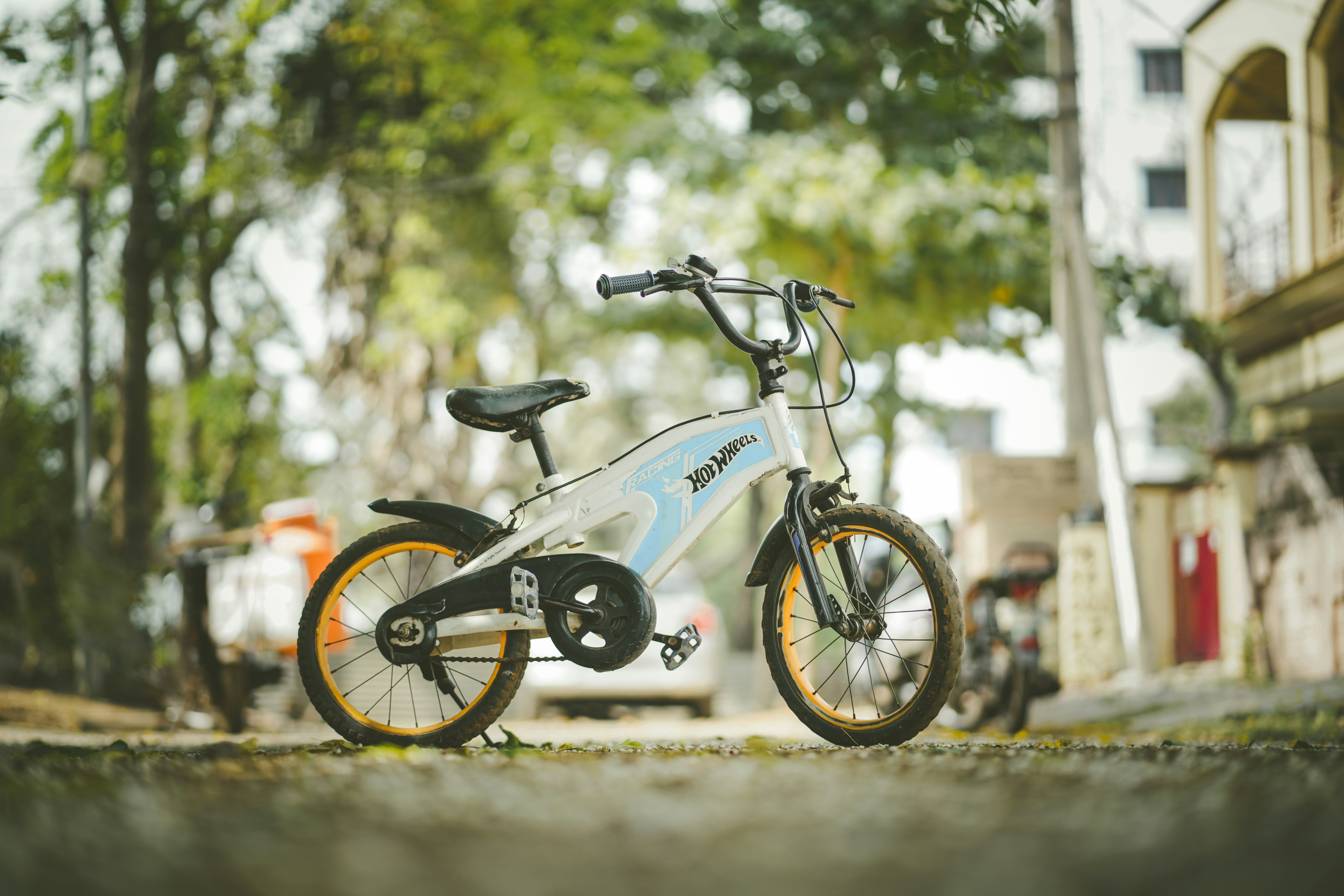 White and blue motorcycle parked on a sunlit dirt road surrounded by urban greenery.