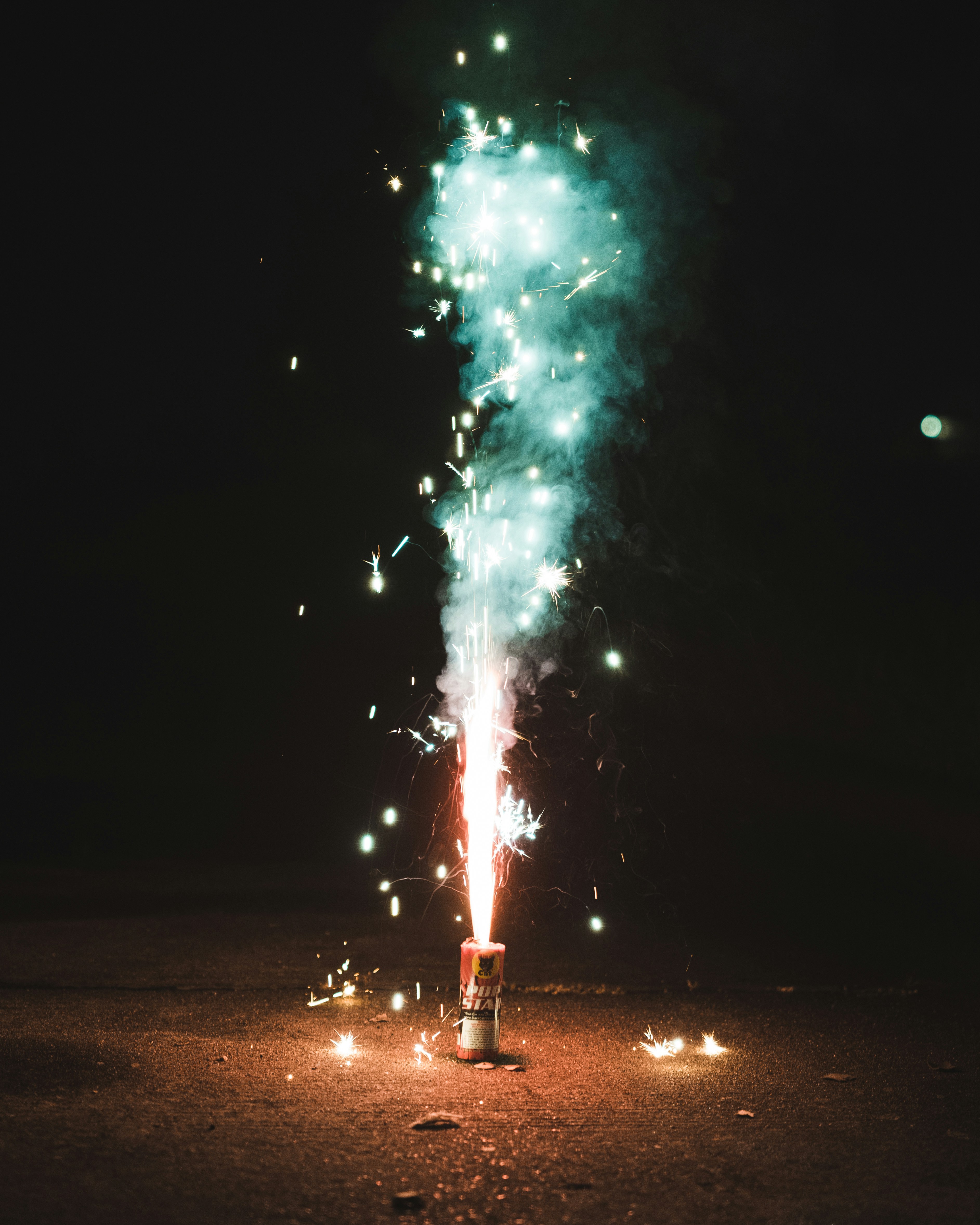 Person standing on sand holding green and white fireworks during night ...
