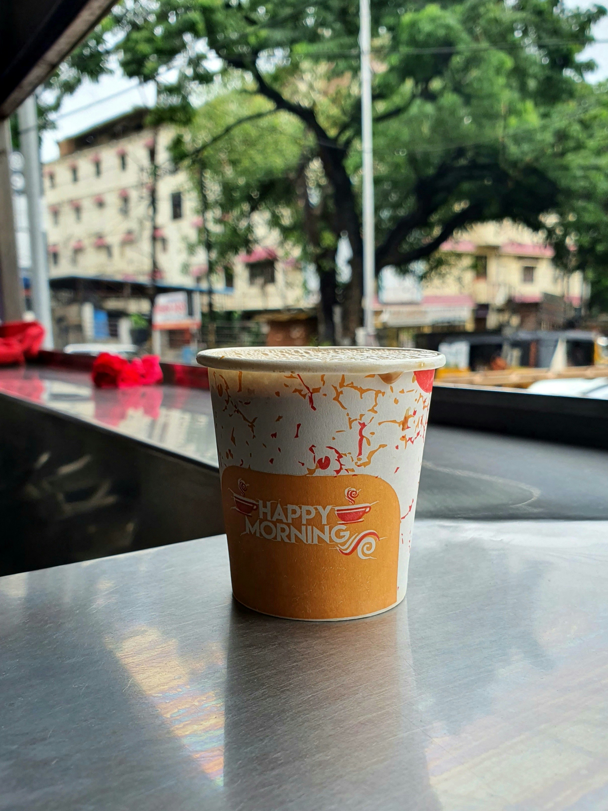Coffee cup with 'HAPPY MORNING' text on a reflective surface, showcasing a bustling street scene in the background.