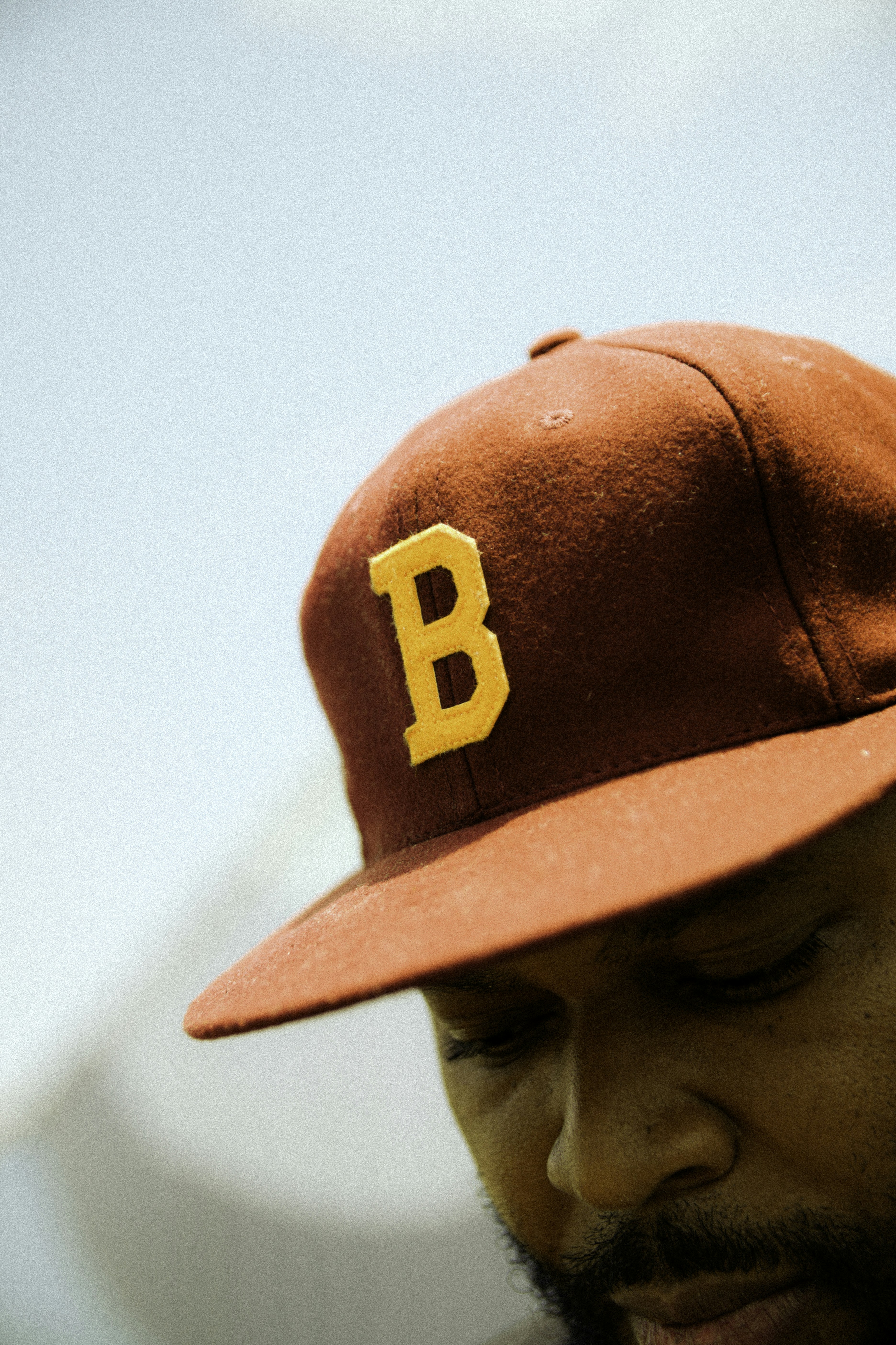 Close-up of a man wearing a brown cap with a yellow 'B', showcasing a contemplative expression against a softly blurred background.