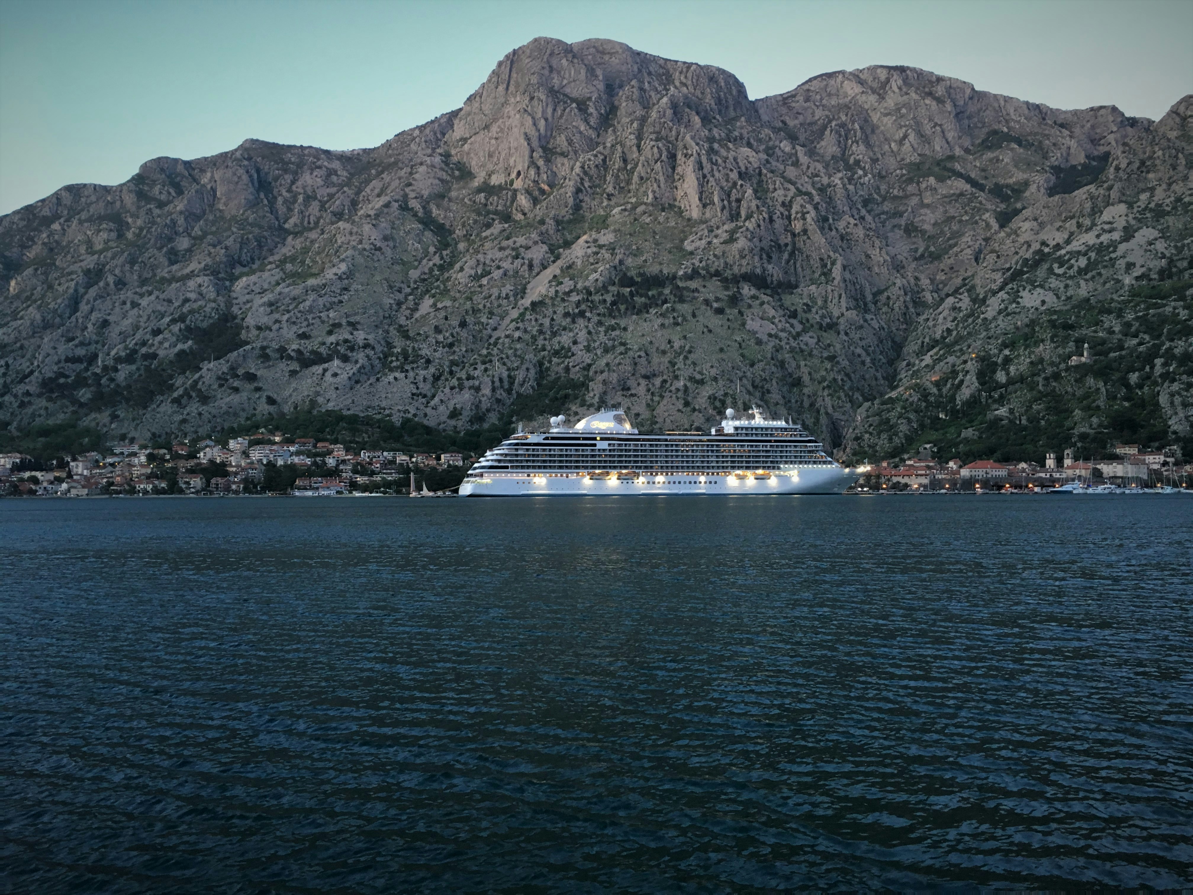 A large cruise ship anchored in tranquil waters, framed by towering mountains at dusk.