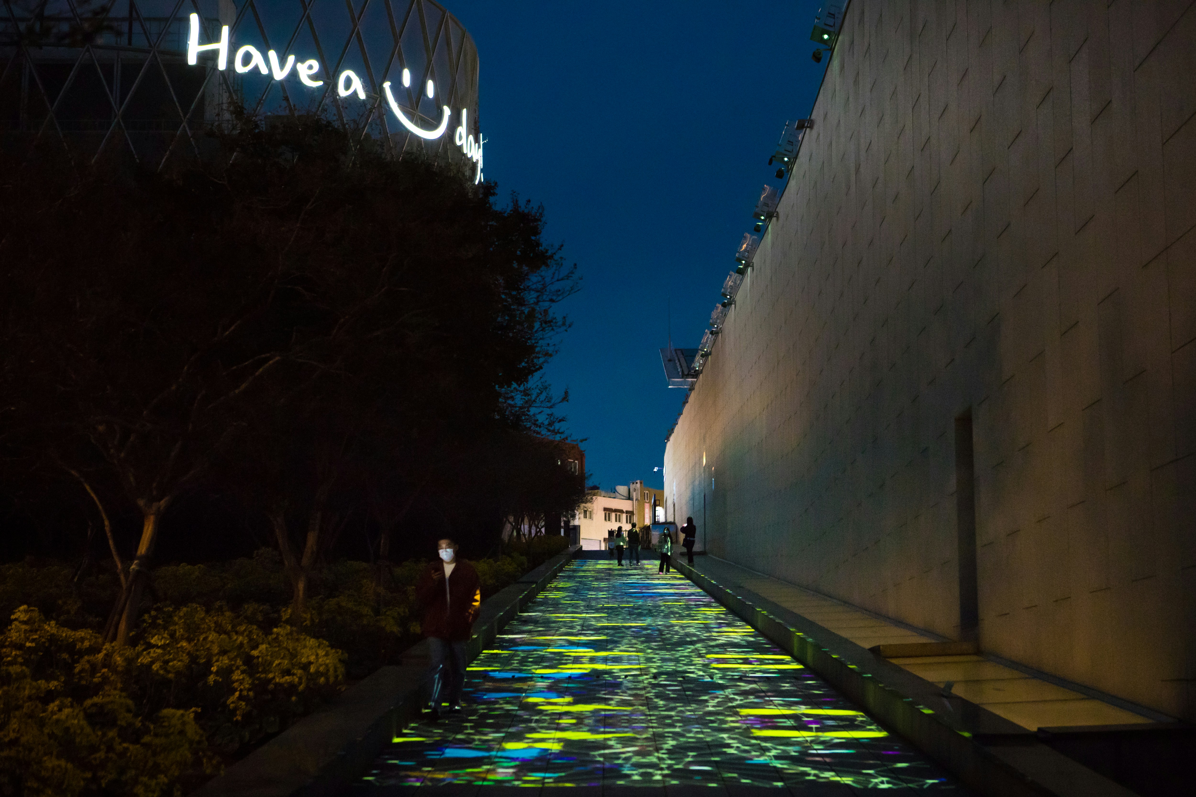 Vibrant, digitally projected patterns illuminate a pathway at night, guiding pedestrians through a modern urban landscape.