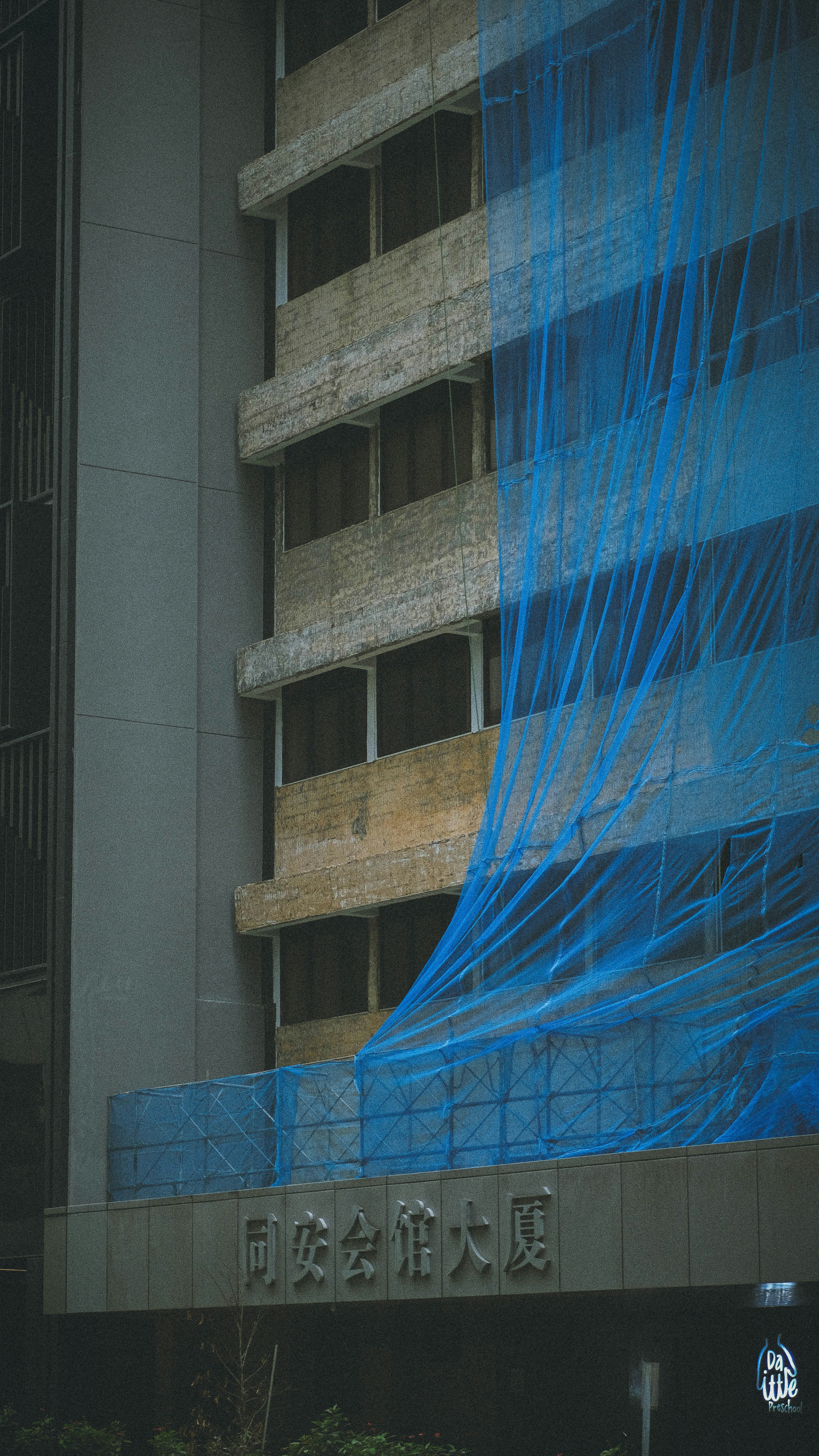A partially obscured building facade draped in blue mesh, hinting at ongoing renovations and urban change.