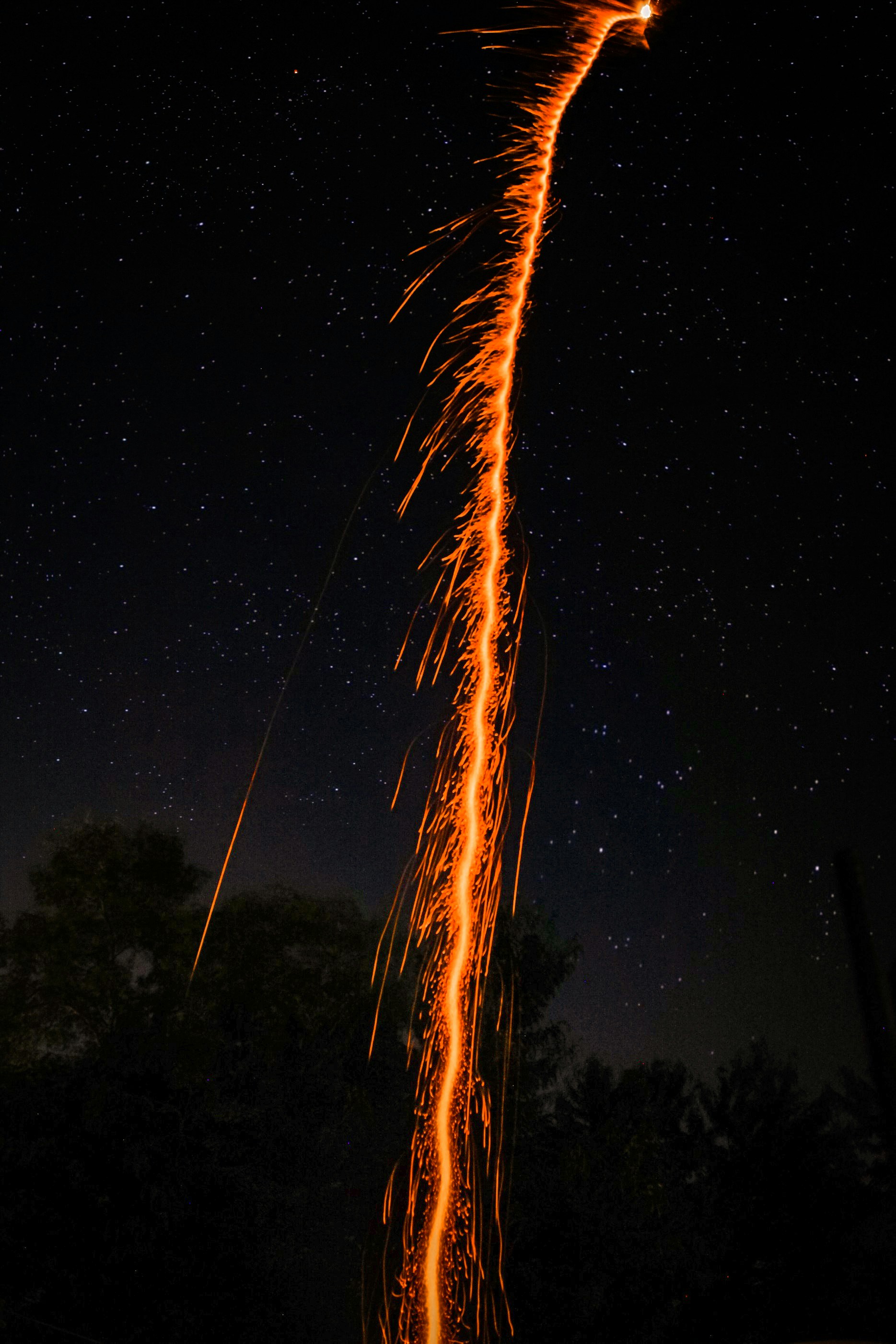A vibrant trail of sparks rises against a star-filled night sky, capturing the dynamic energy of a firework display.