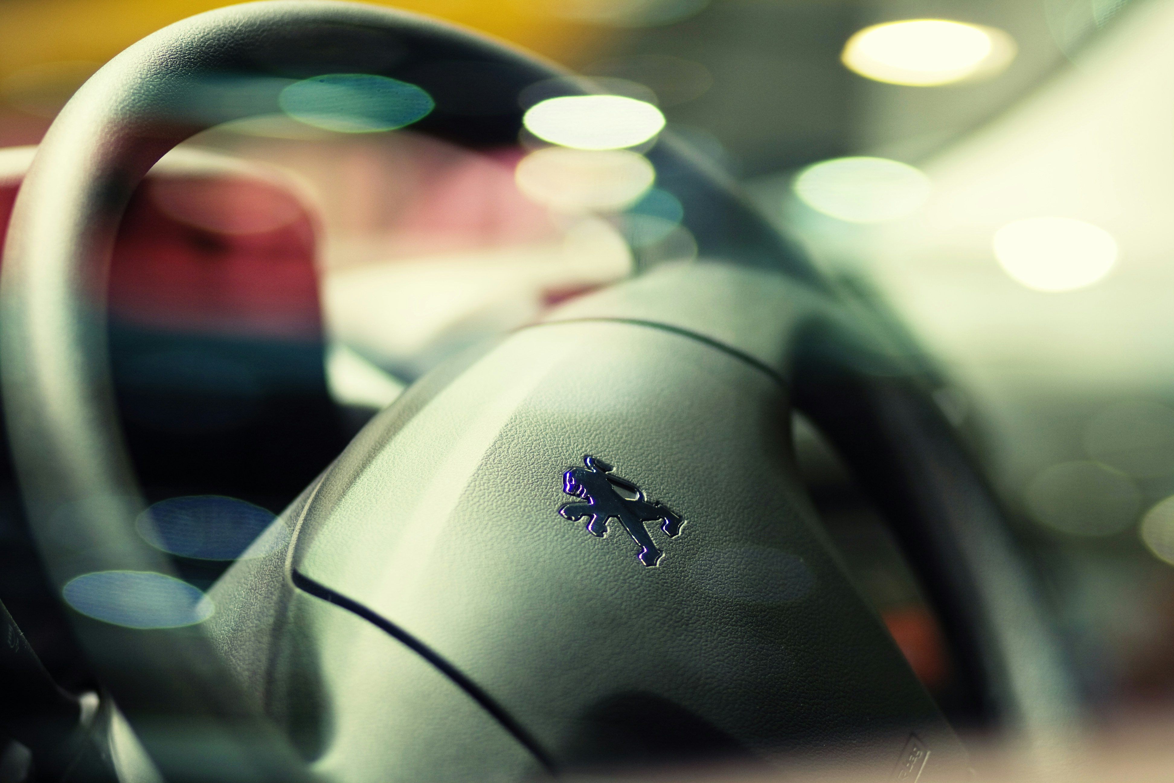 Close-up of a car steering wheel featuring the Peugeot logo, with blurred lights reflecting in the background. 