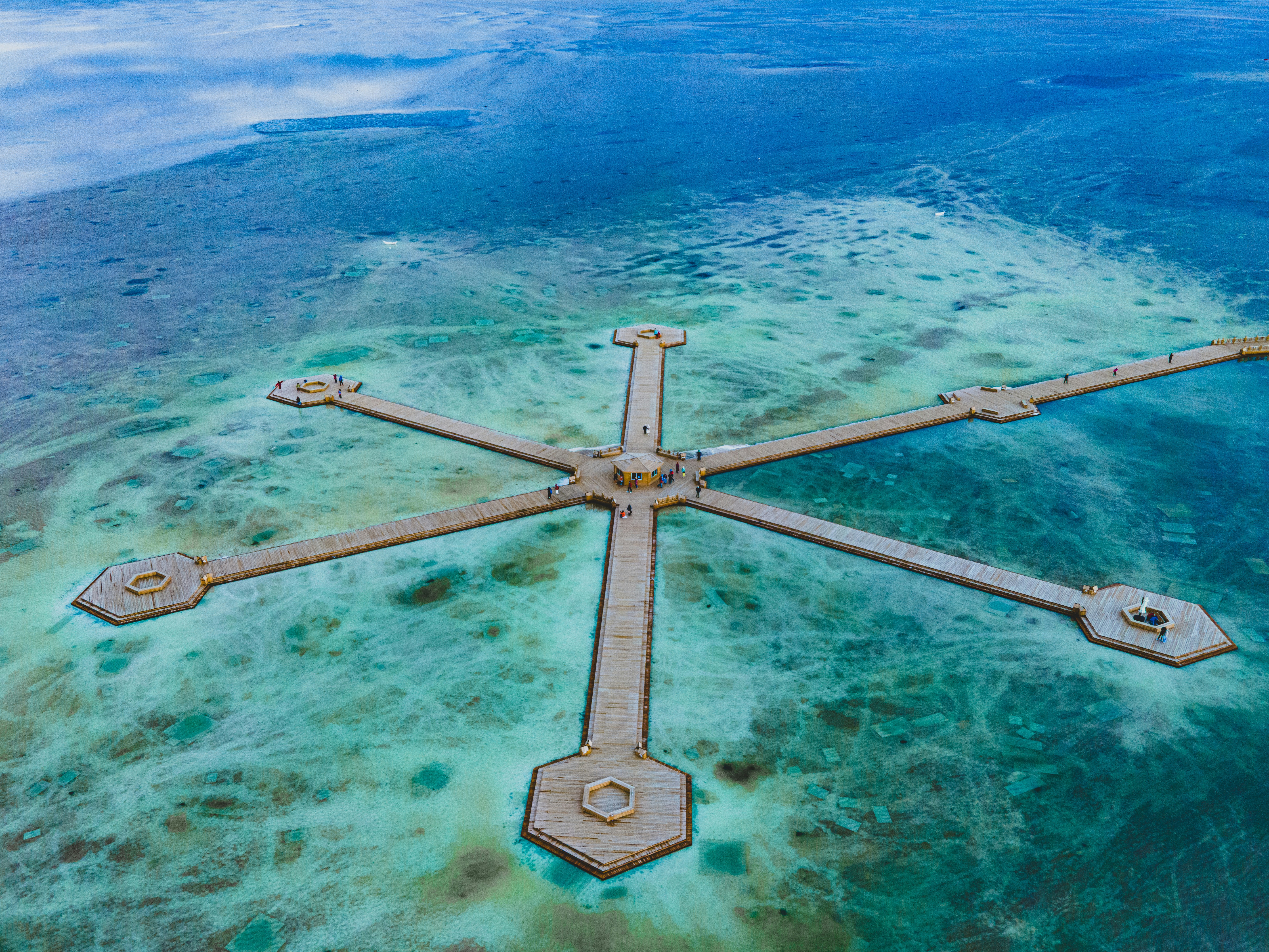 Aerial view of a hexagonal wooden pier extending into turquoise waters, surrounded by vibrant marine life. The structure invites exploration and tranquility.
