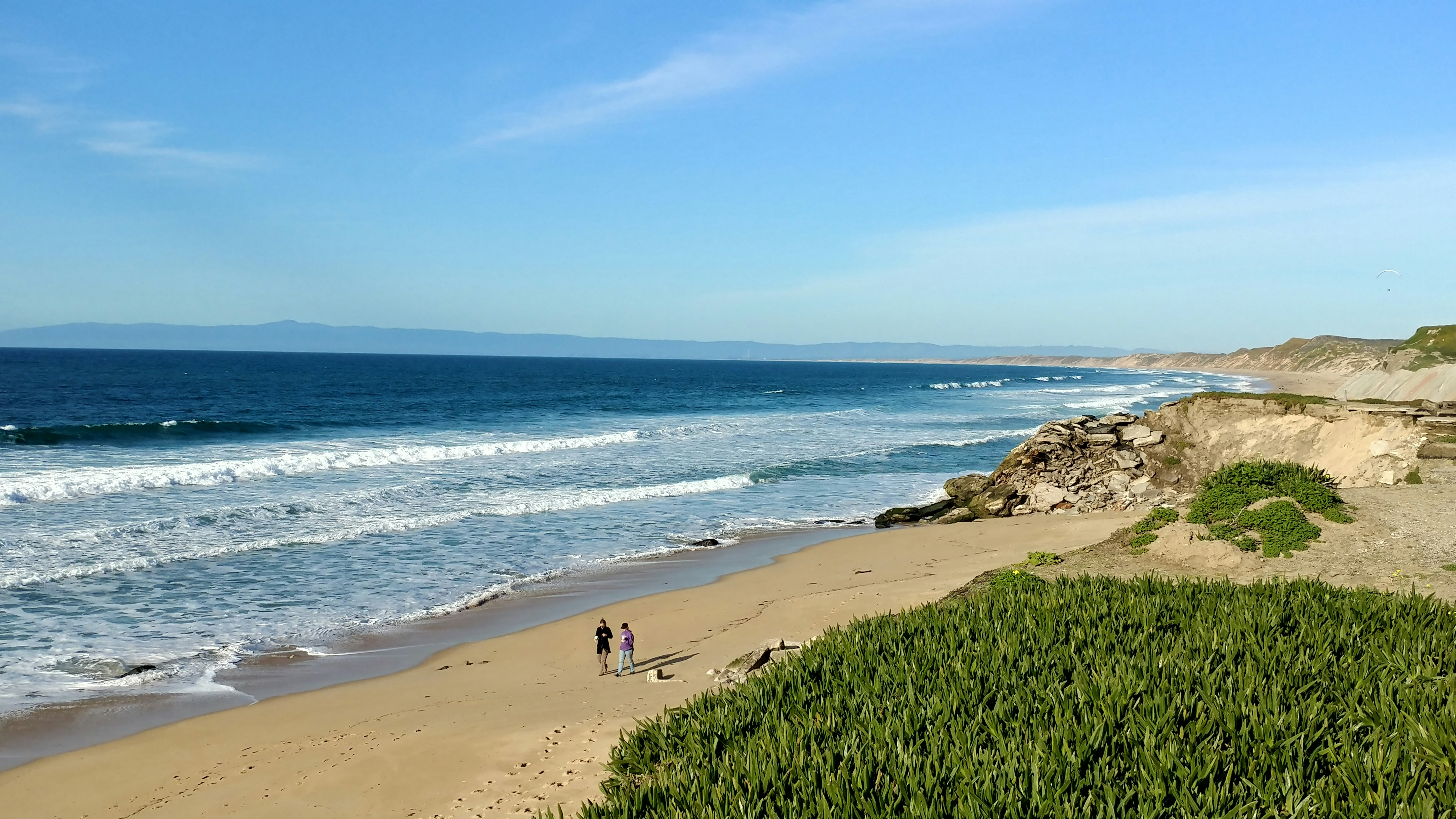 Expansive beach with gentle waves and cliffs under a clear blue sky.
