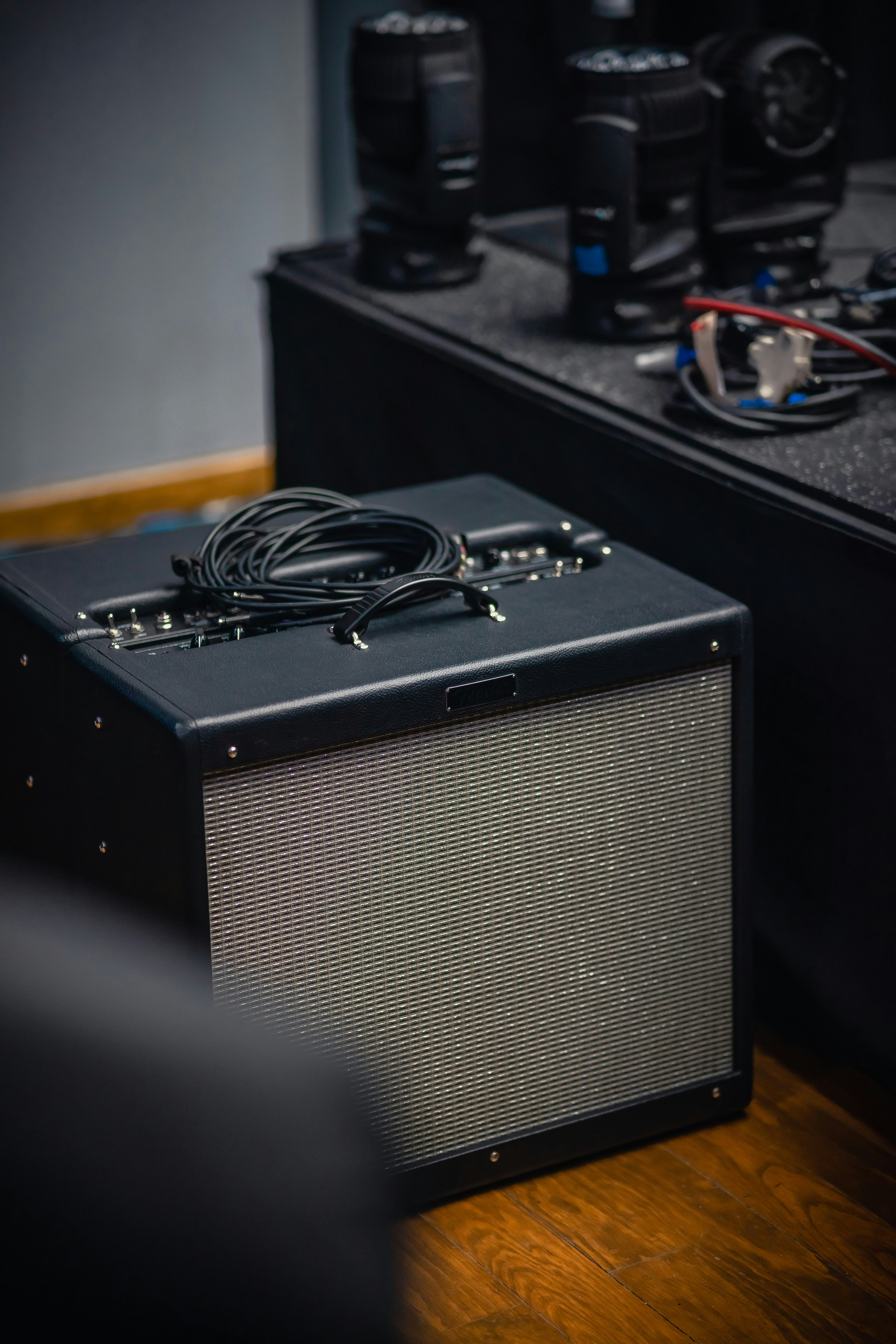 A black guitar amplifier sits prominently on a wooden floor, surrounded by camera equipment and cables, illustrating a creative workspace.