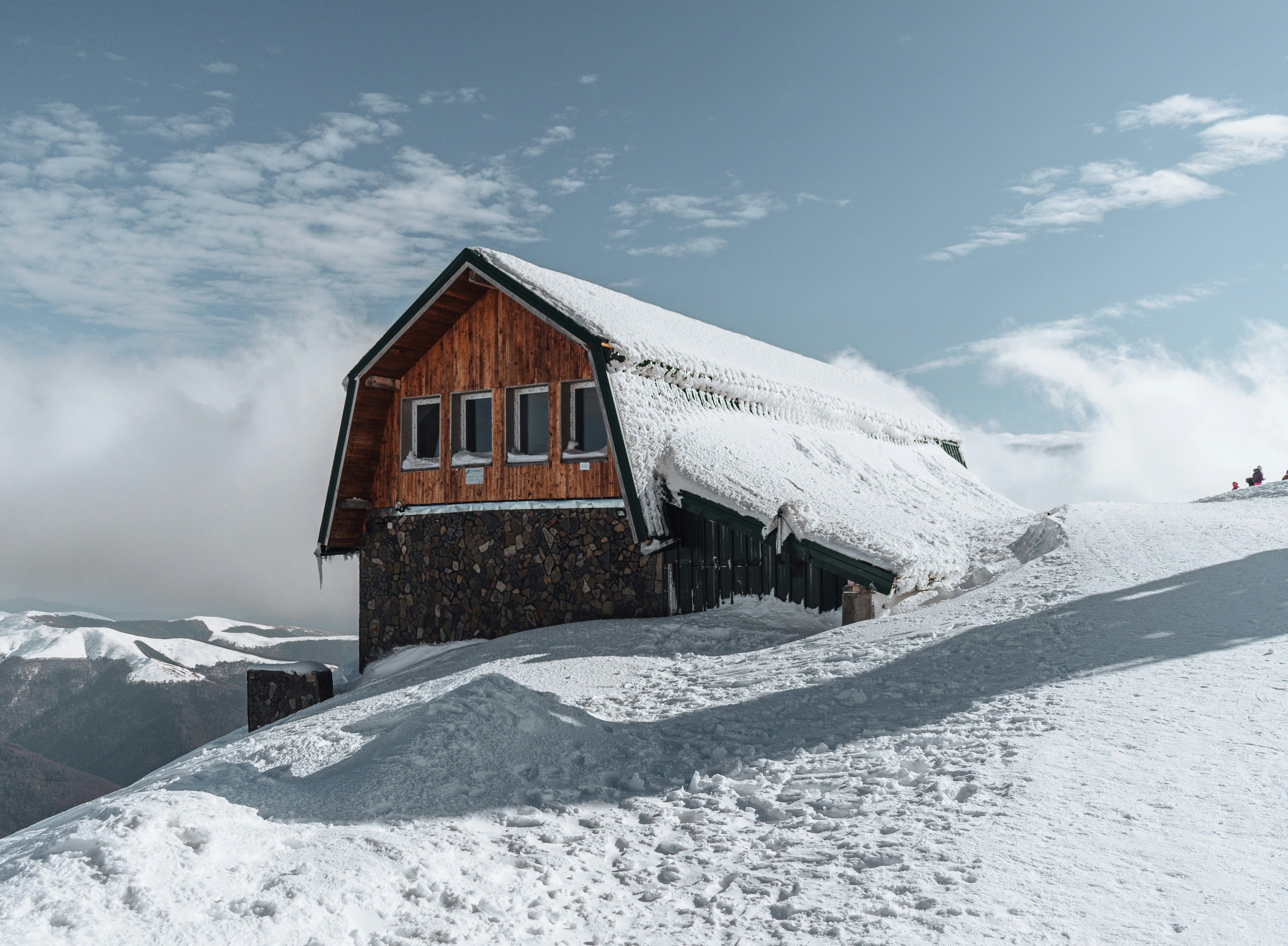 Charming wooden cabin with a snow-covered roof nestled in a serene mountain landscape under a clear sky.