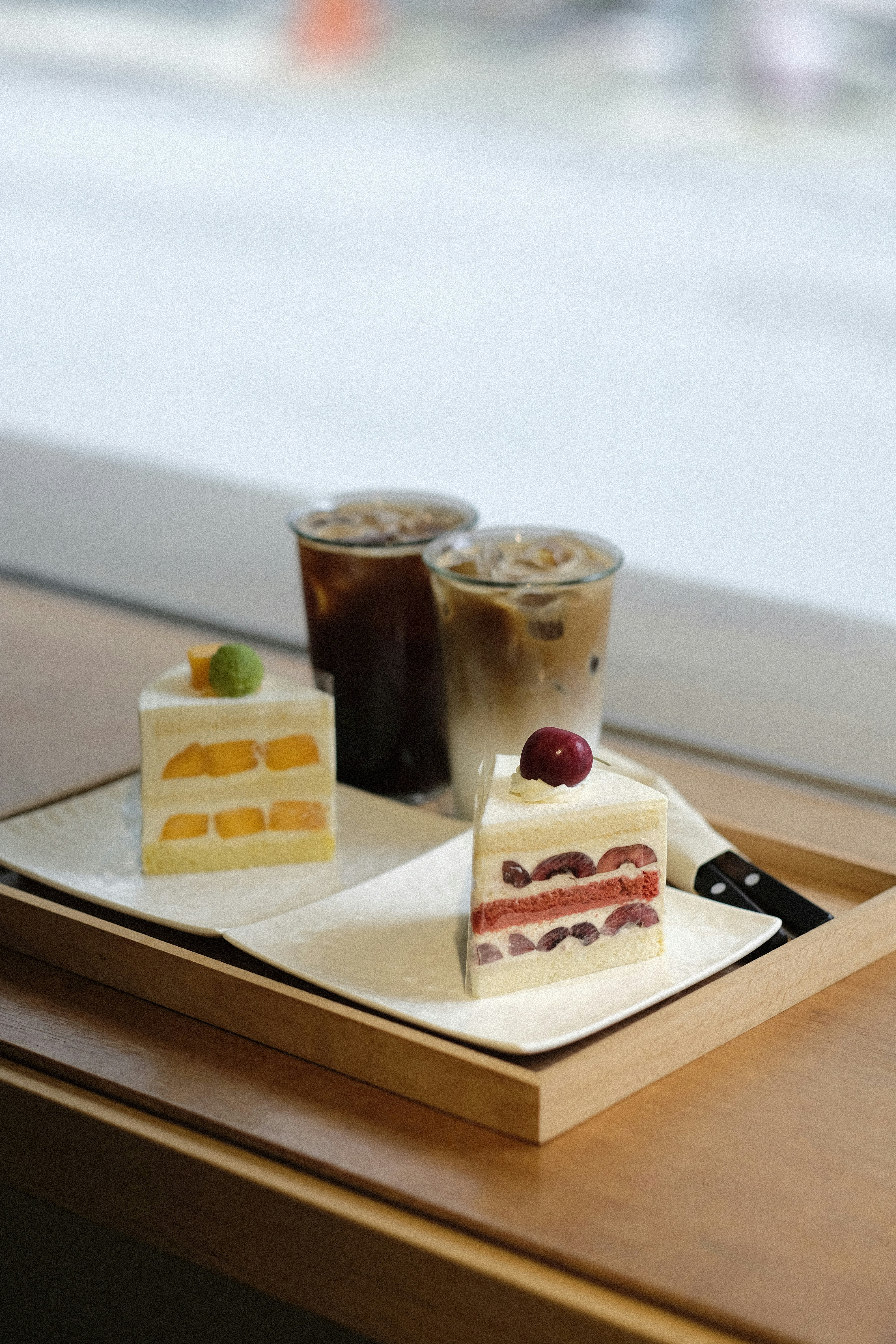 Dessert Duet: Mango-layer and Berry-layer Cakes Framed by Iced Coffee on a Wooden Tray