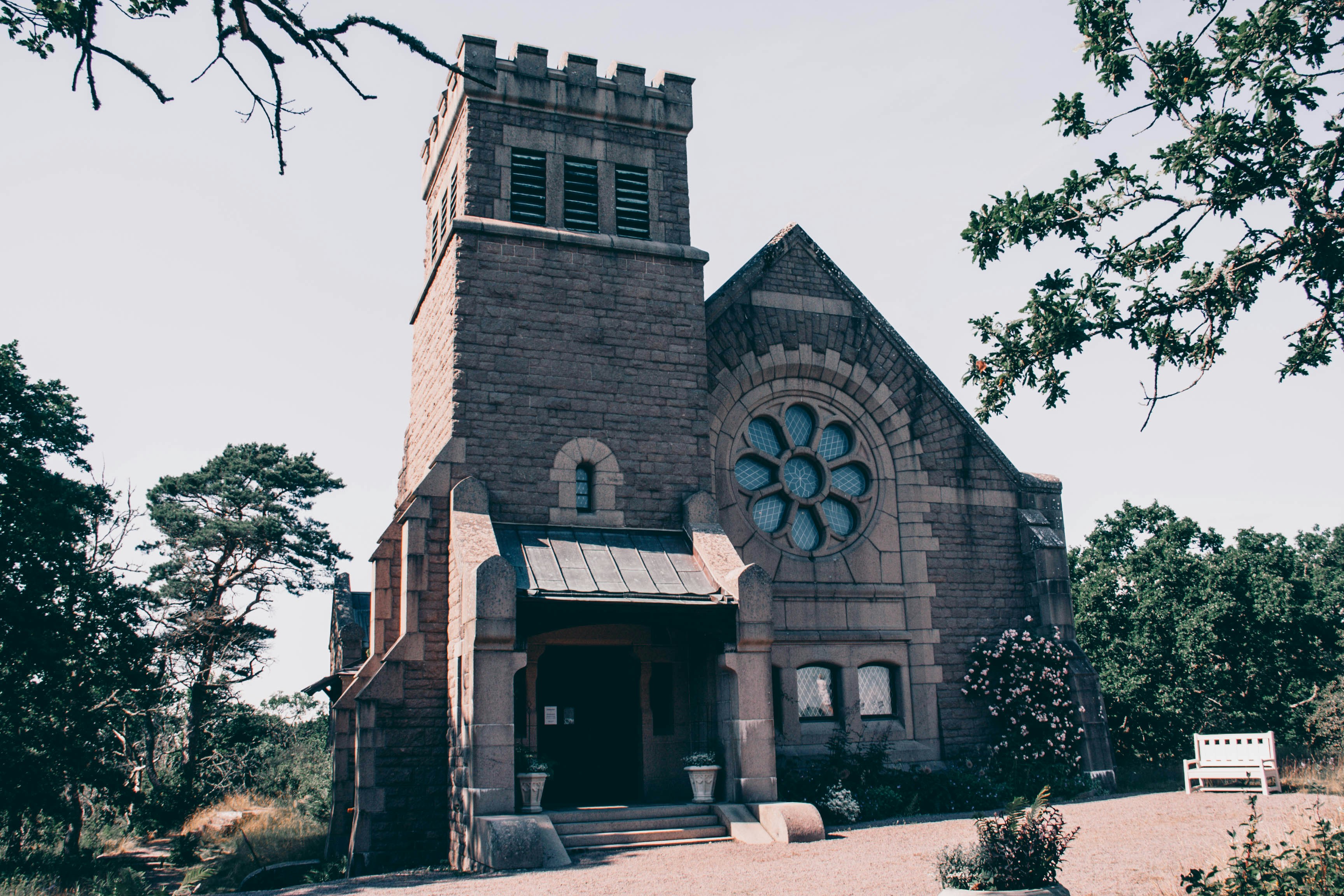 Historic stone chapel nestled among trees, featuring a large circular window and a welcoming entrance.
