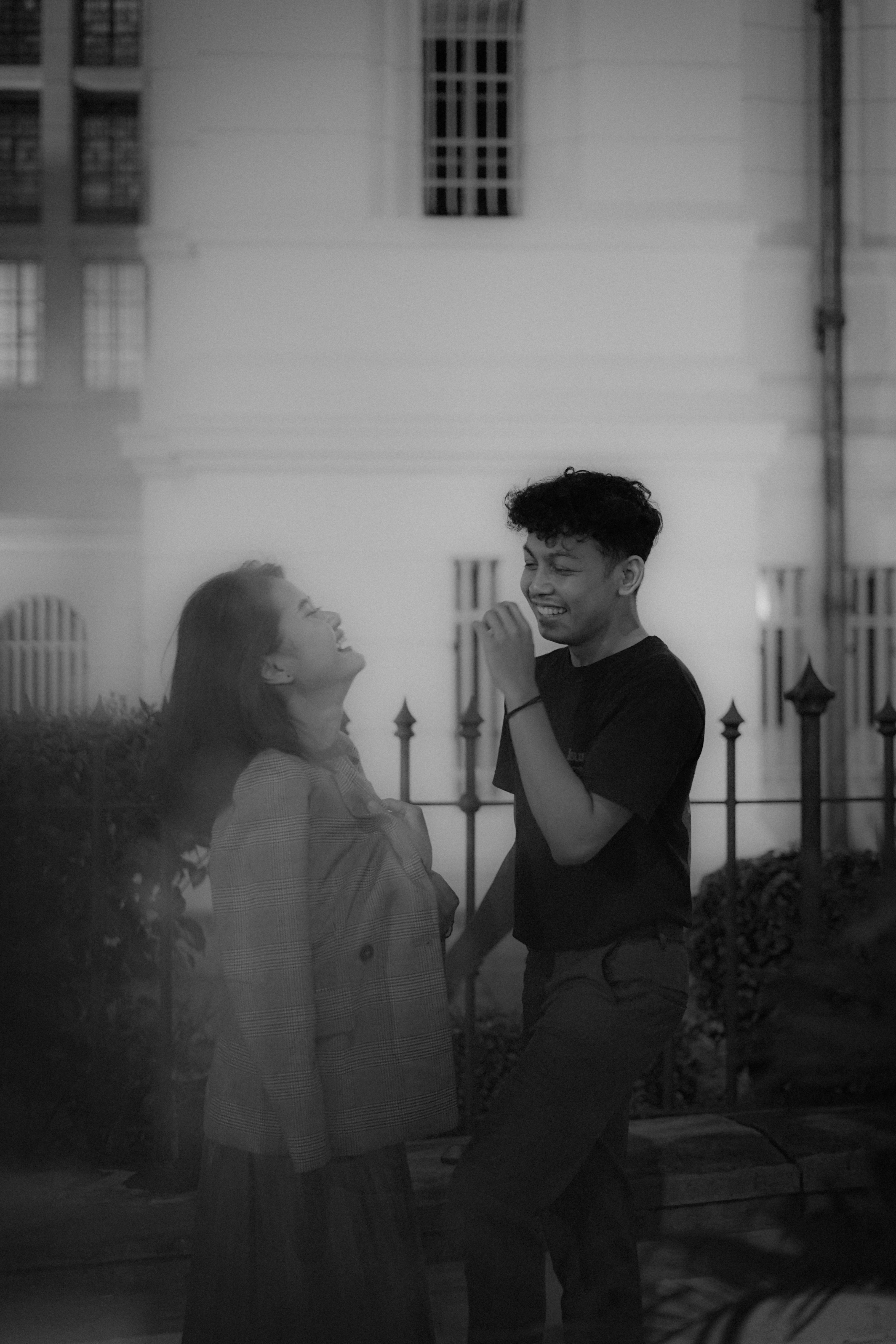 Two friends share a moment of laughter outdoors, captured in black and white, highlighting their expressions against a softly blurred backdrop.